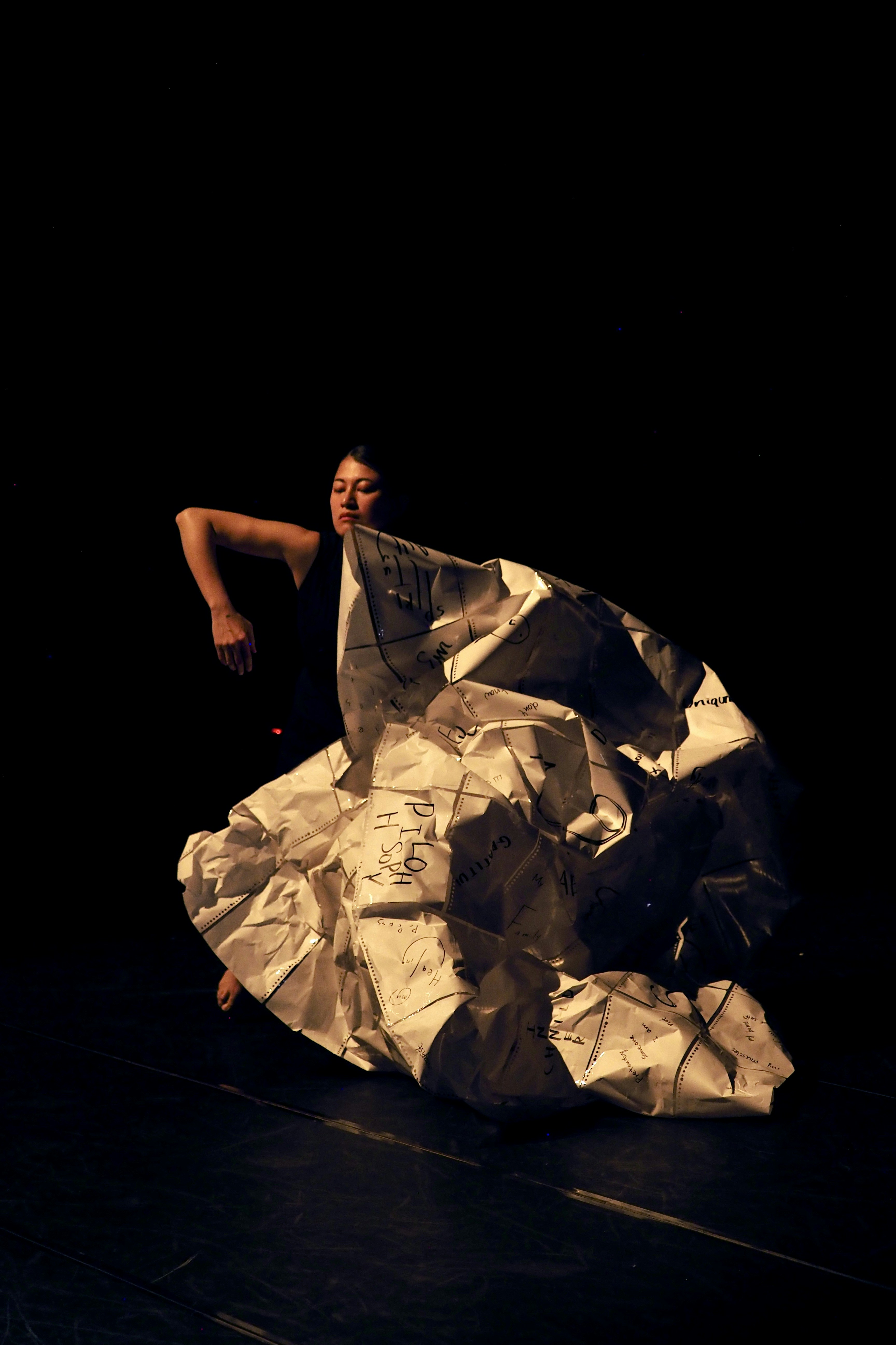 Silhouetted Dancer Wrapped in Metallic Crumple-Tape Fabric on a Dark Stage
