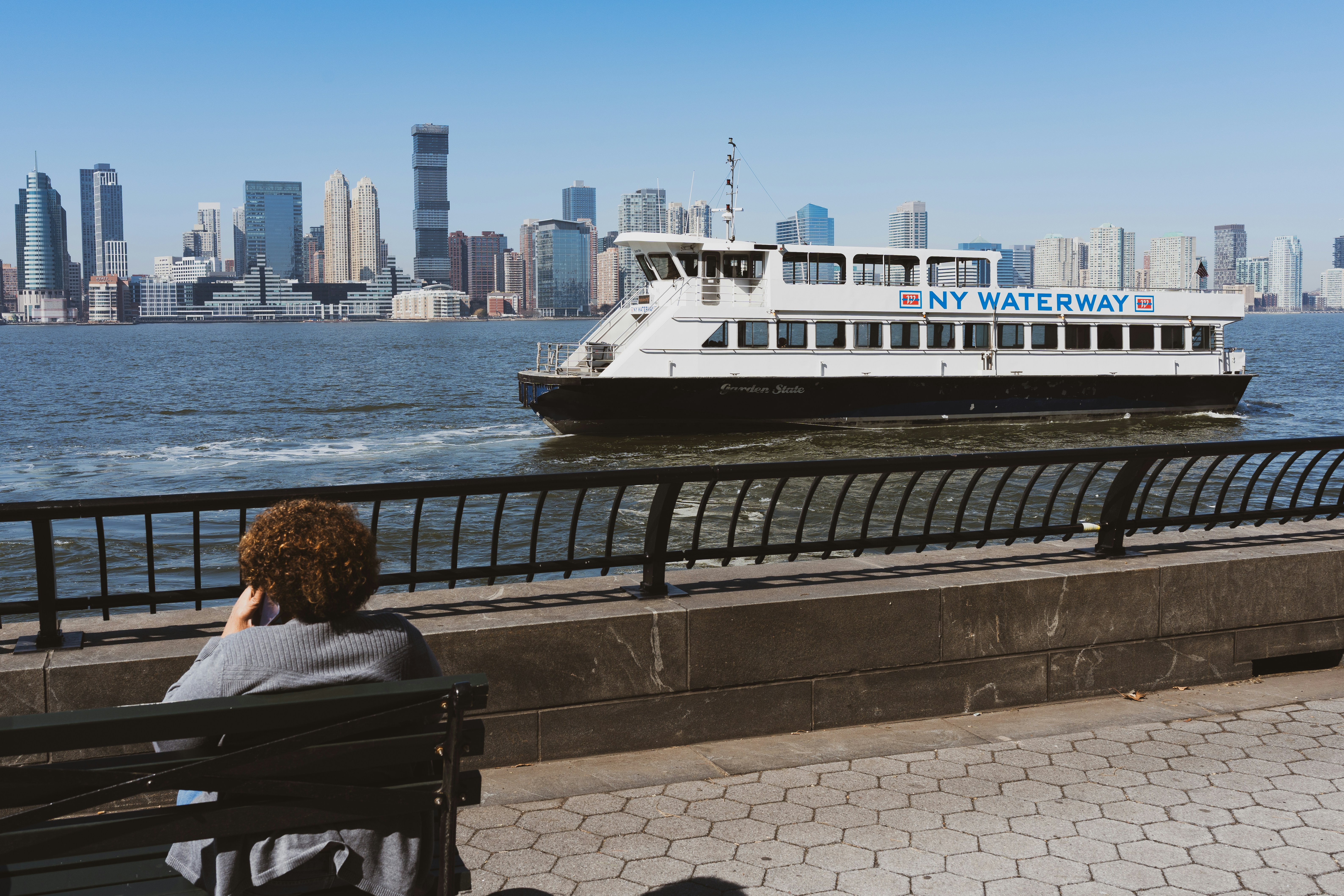 Benchside View: A Passenger Gazes Toward the Waterfront Cityscape