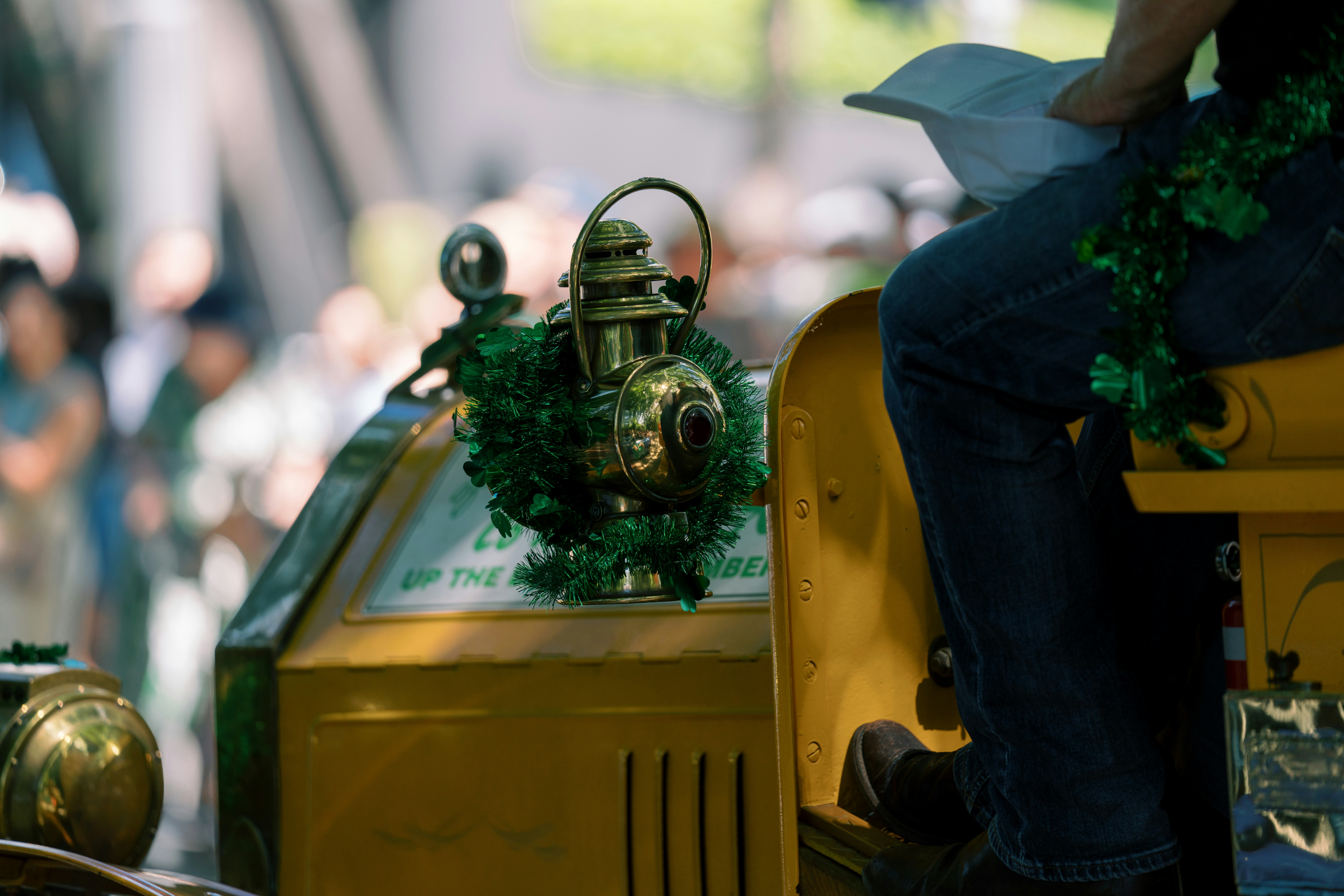 Green garlanded lantern on vintage yellow machinery at a crowded parade