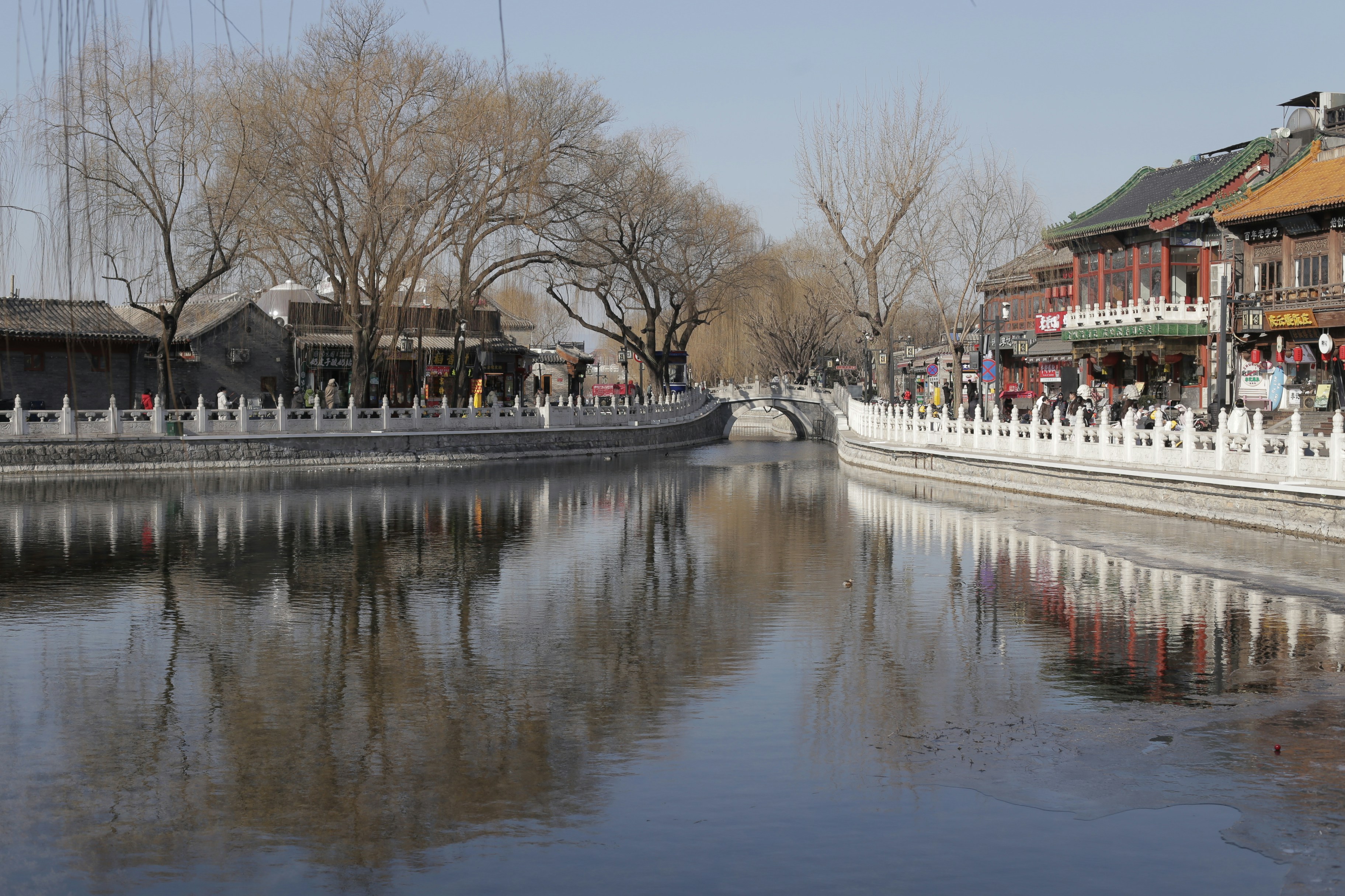 Reflective Riverside: Trees, Boats, and Traditional Architecture Framing the Calm Water