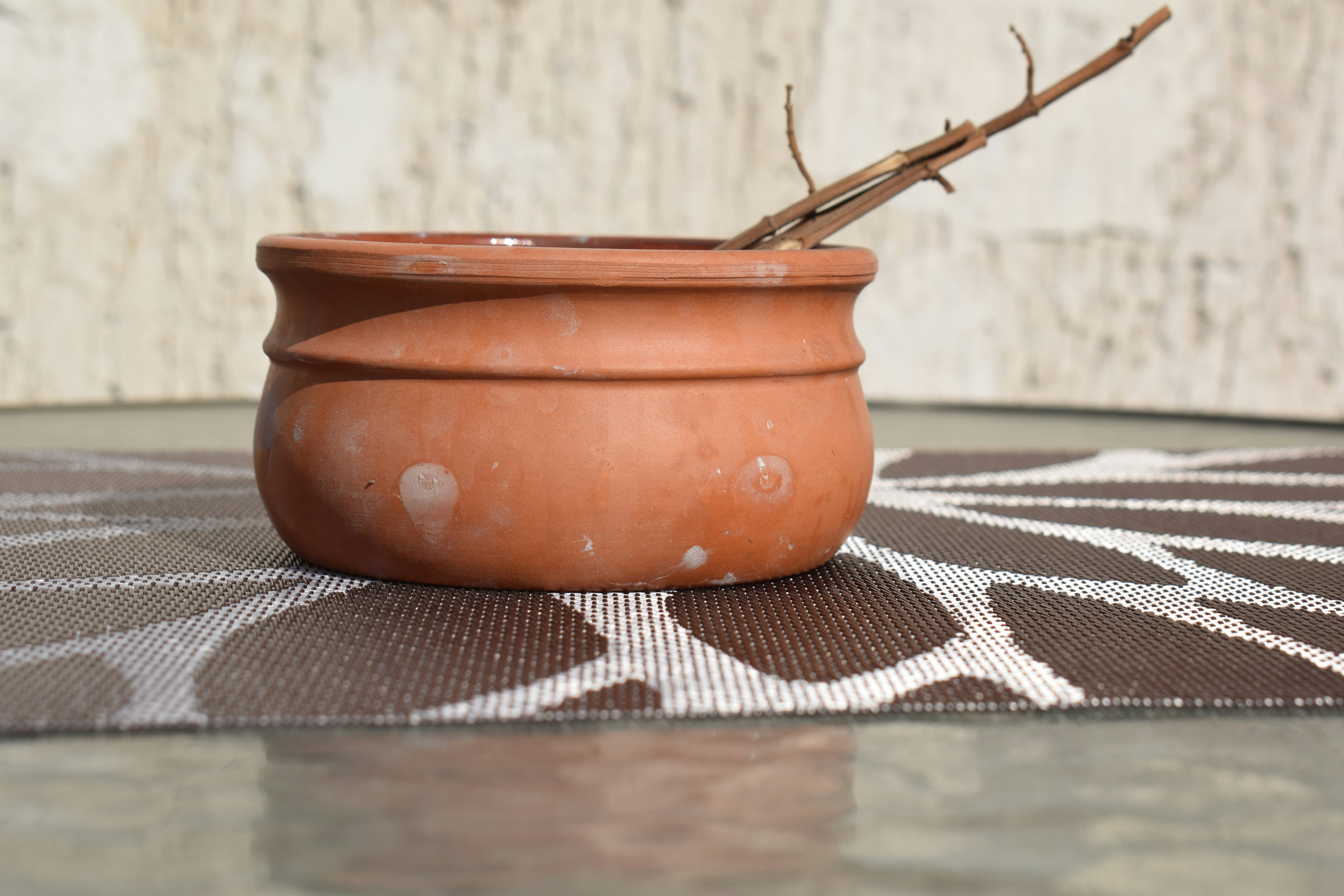 Terra Cotta Vessel with Bare Twig Adornments on Geometric Mat Surface