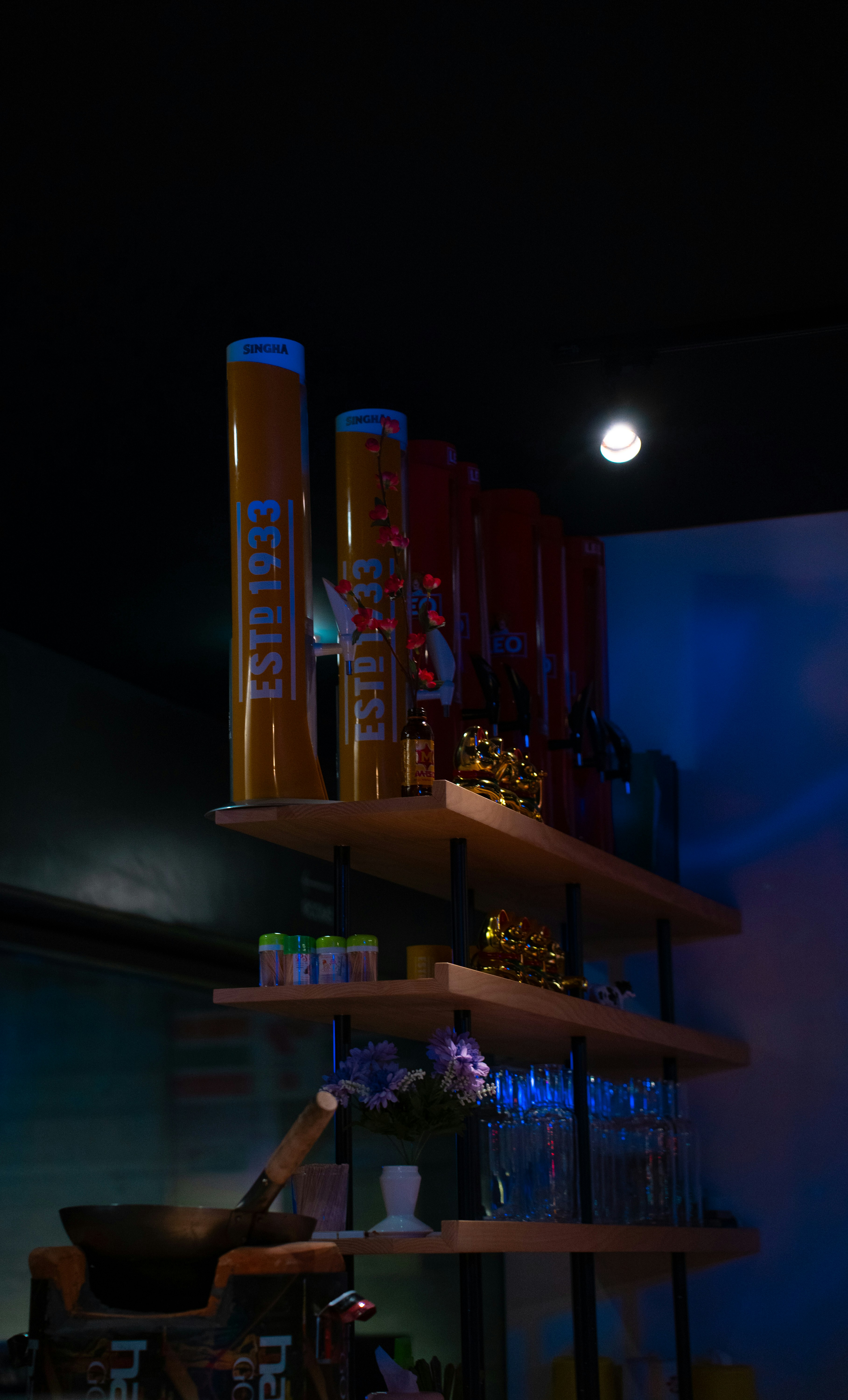 Shelf of Colorful Bottles in a Dim, Neon-Blue Corner