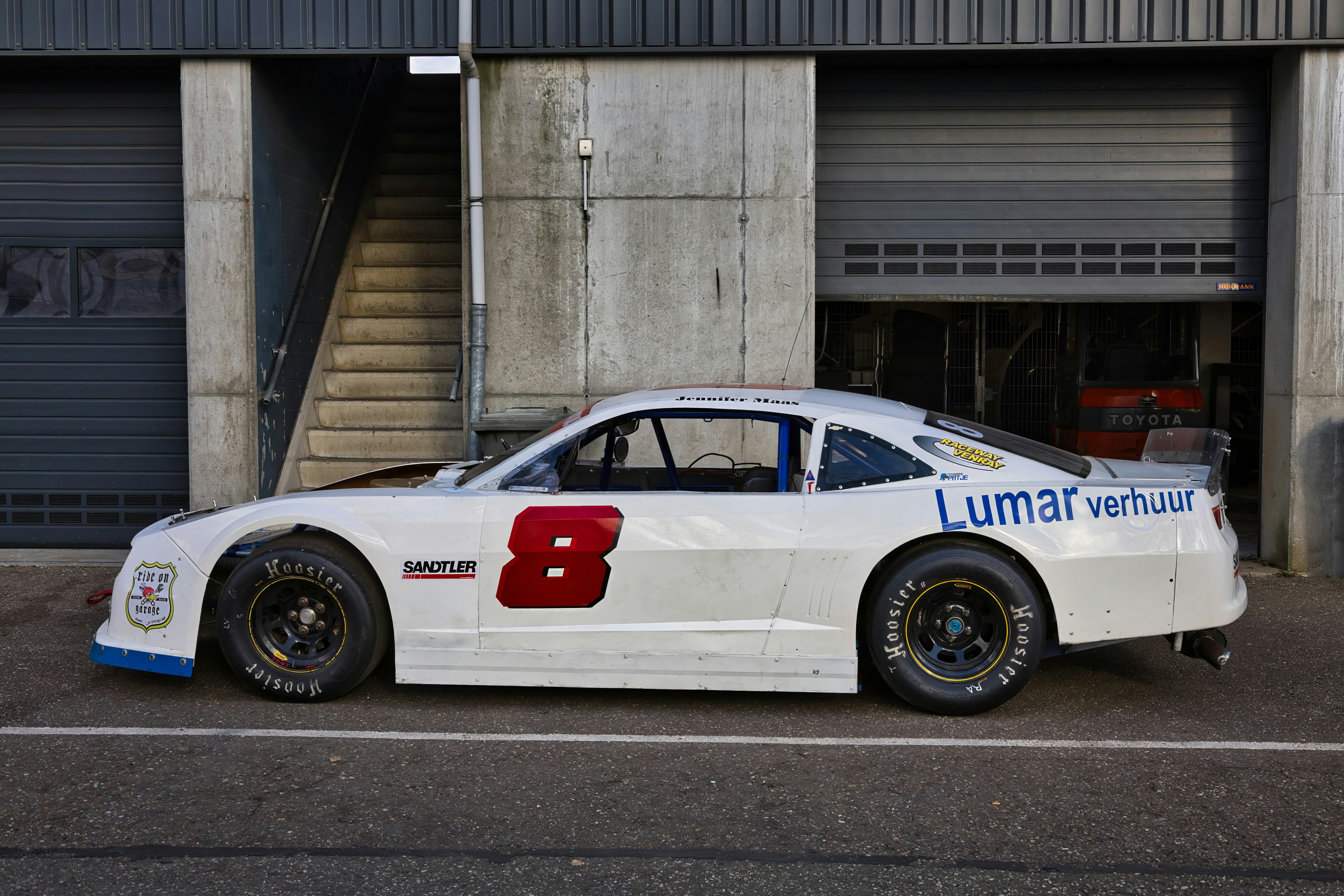 White race car with red number 8 in a garage bay