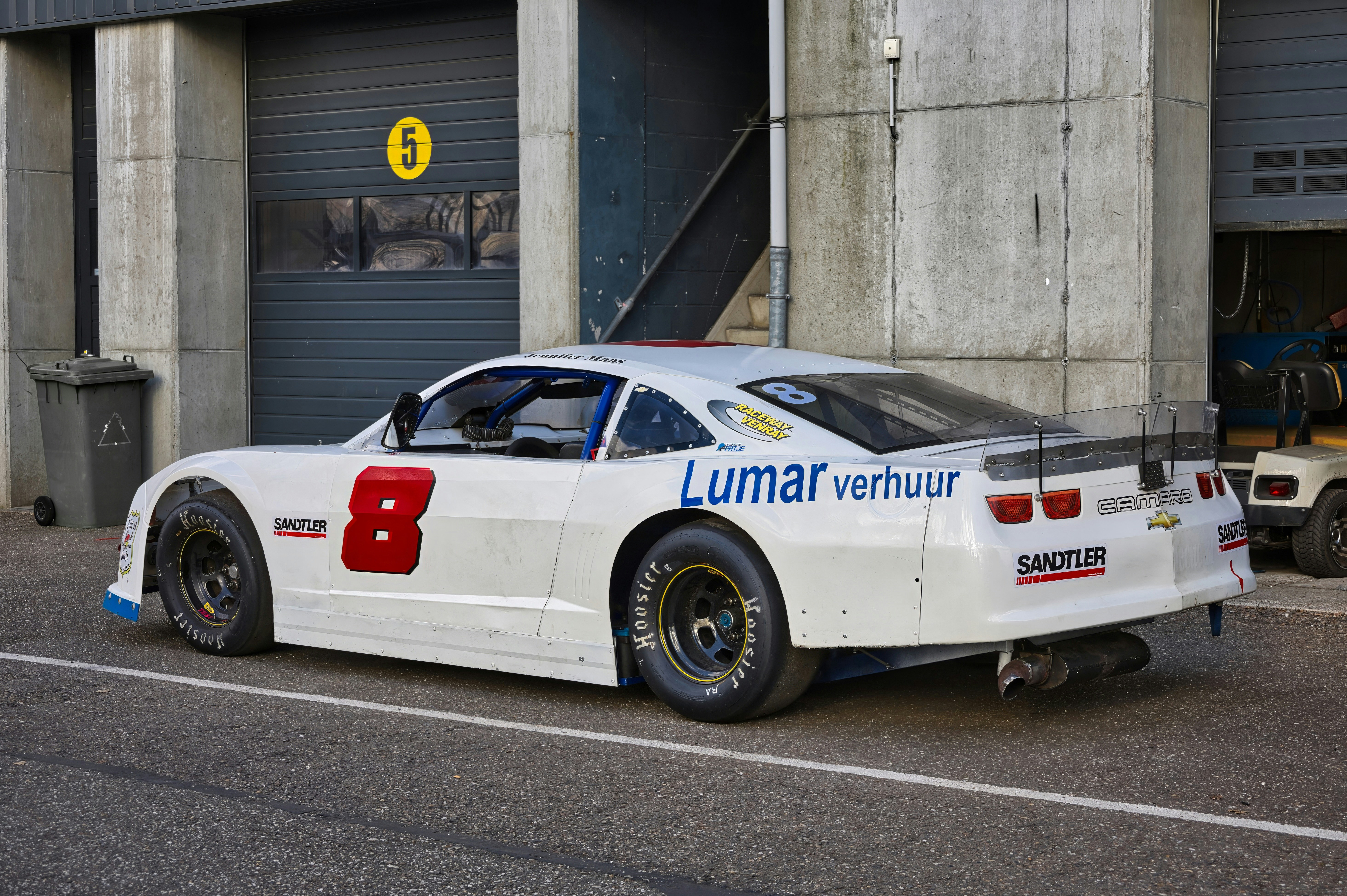 White race car with red number 8 resting in a pit area