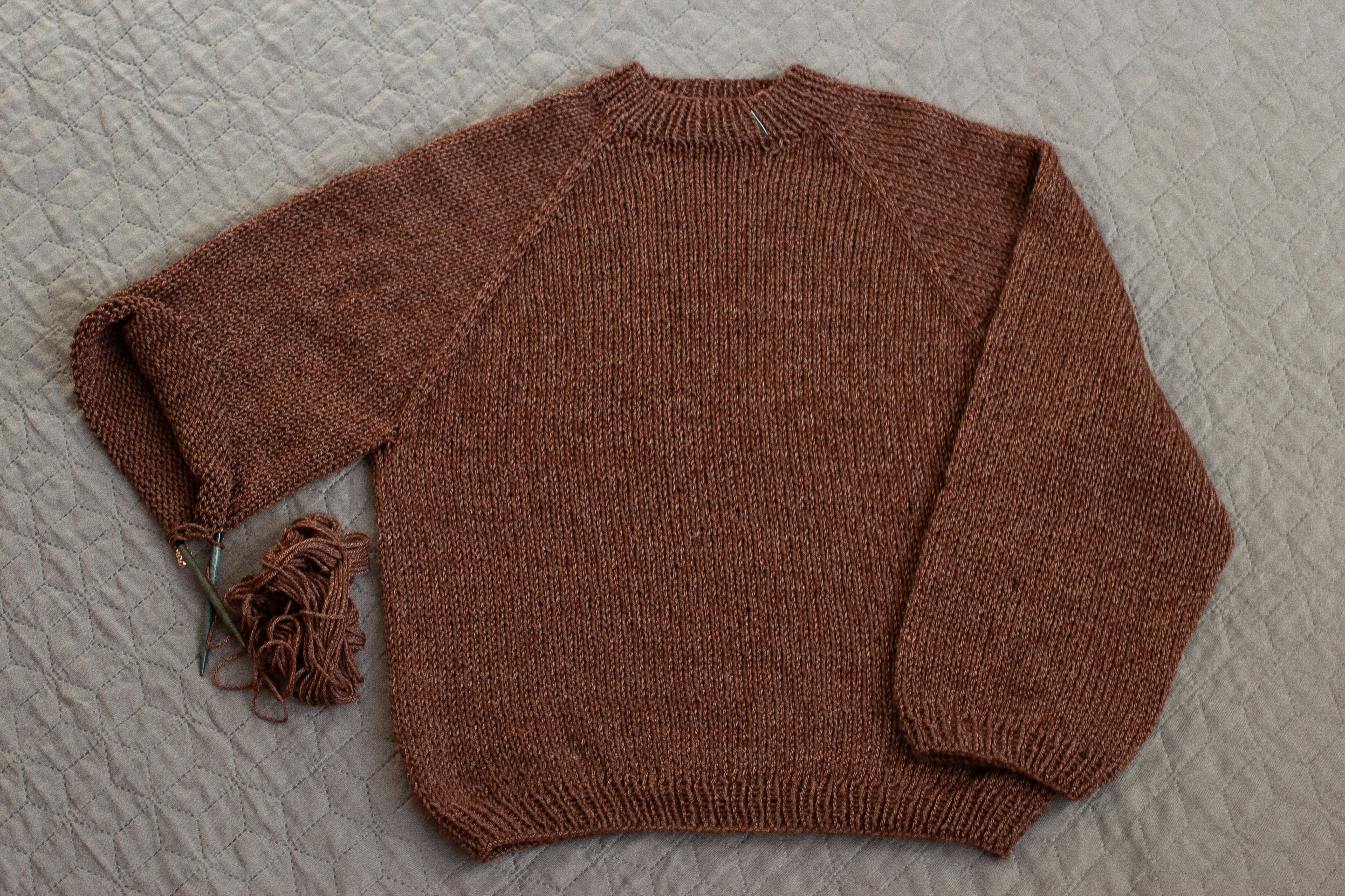 Rustic Knit: A Cozy Brown Sweater Resting on a Quilted Surface