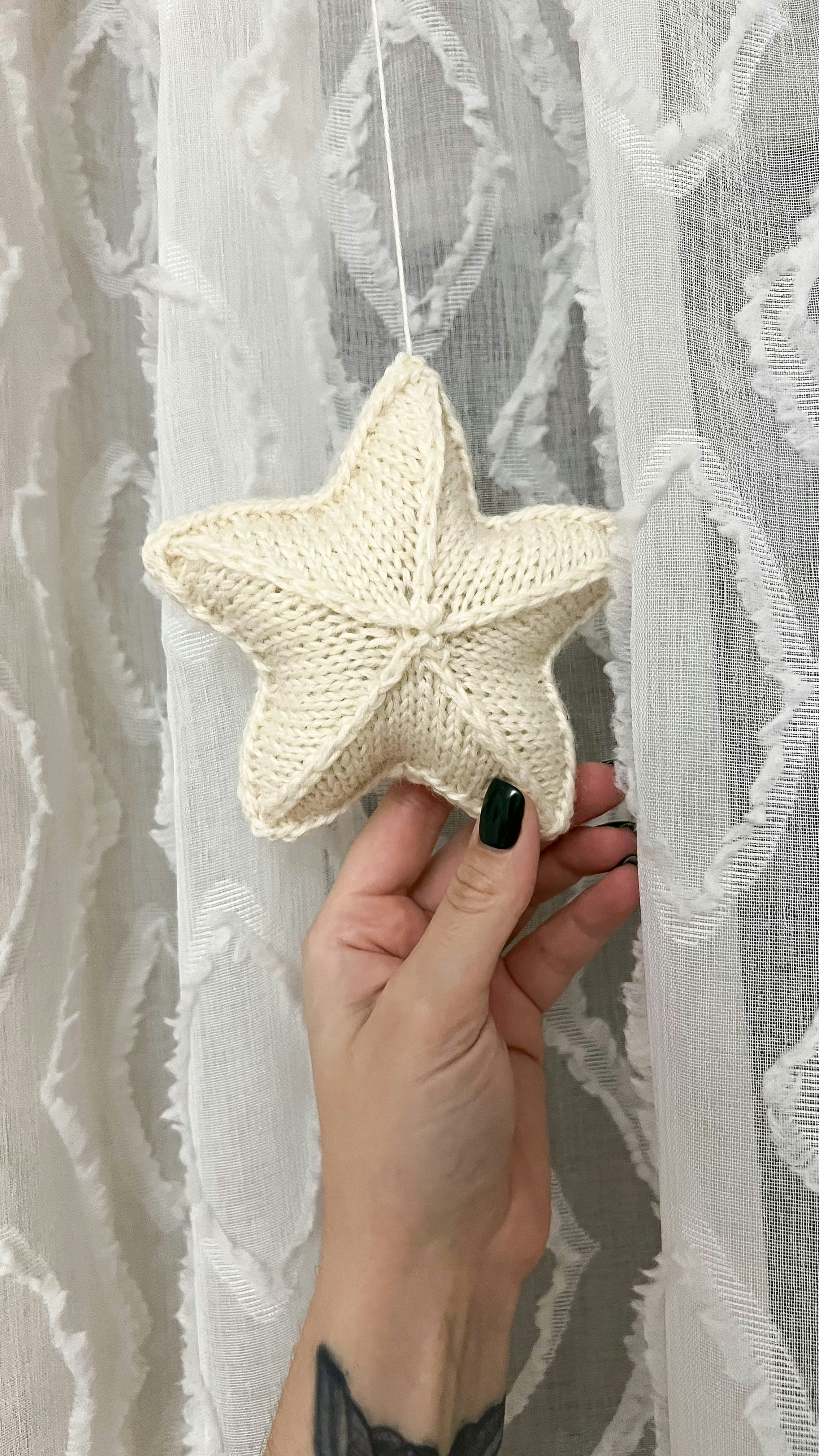 Hand-stitched Star Pendant Grasped in Front of Lace Curtains