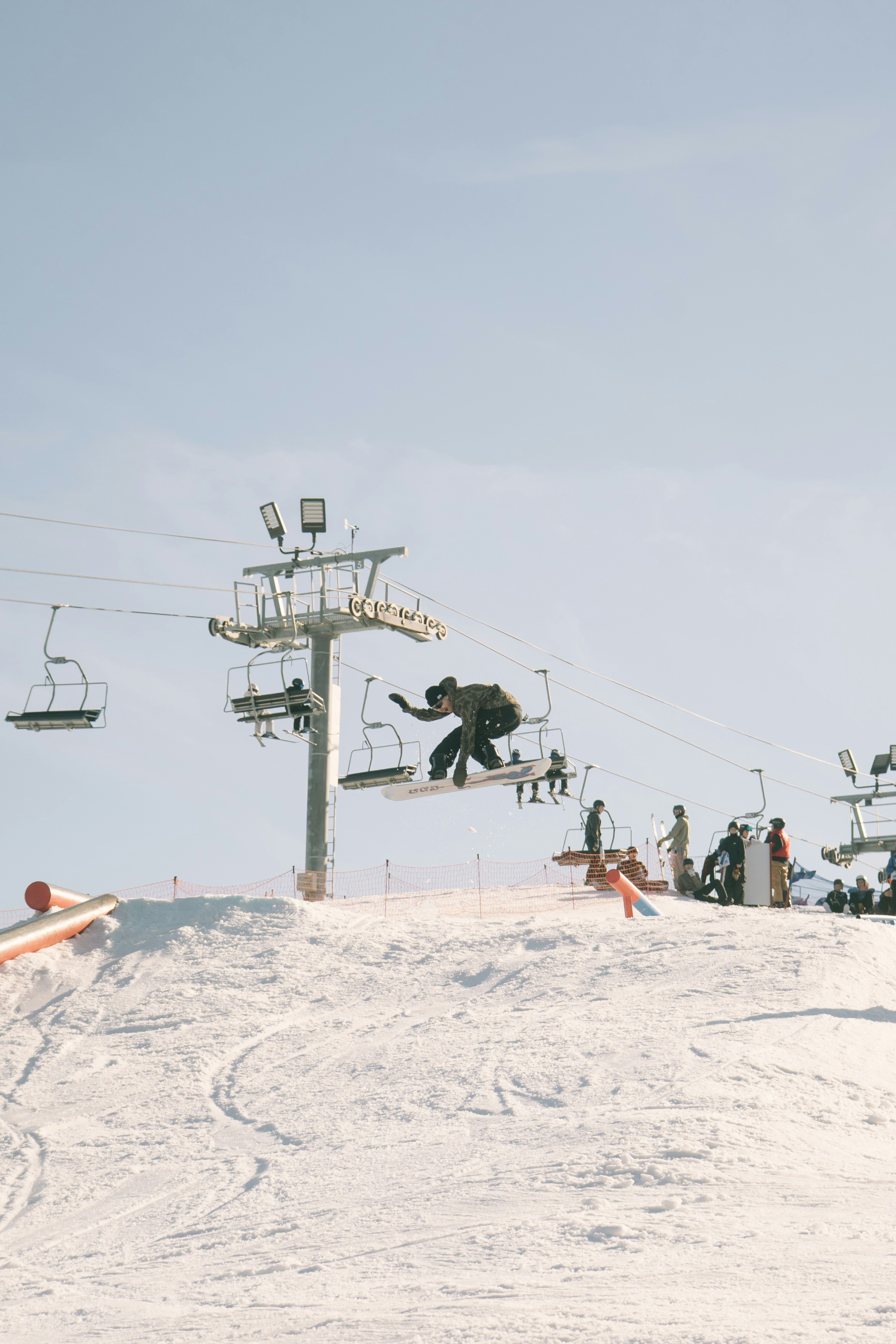 Snowboarder in midair under a chairlift at ski resort dusk