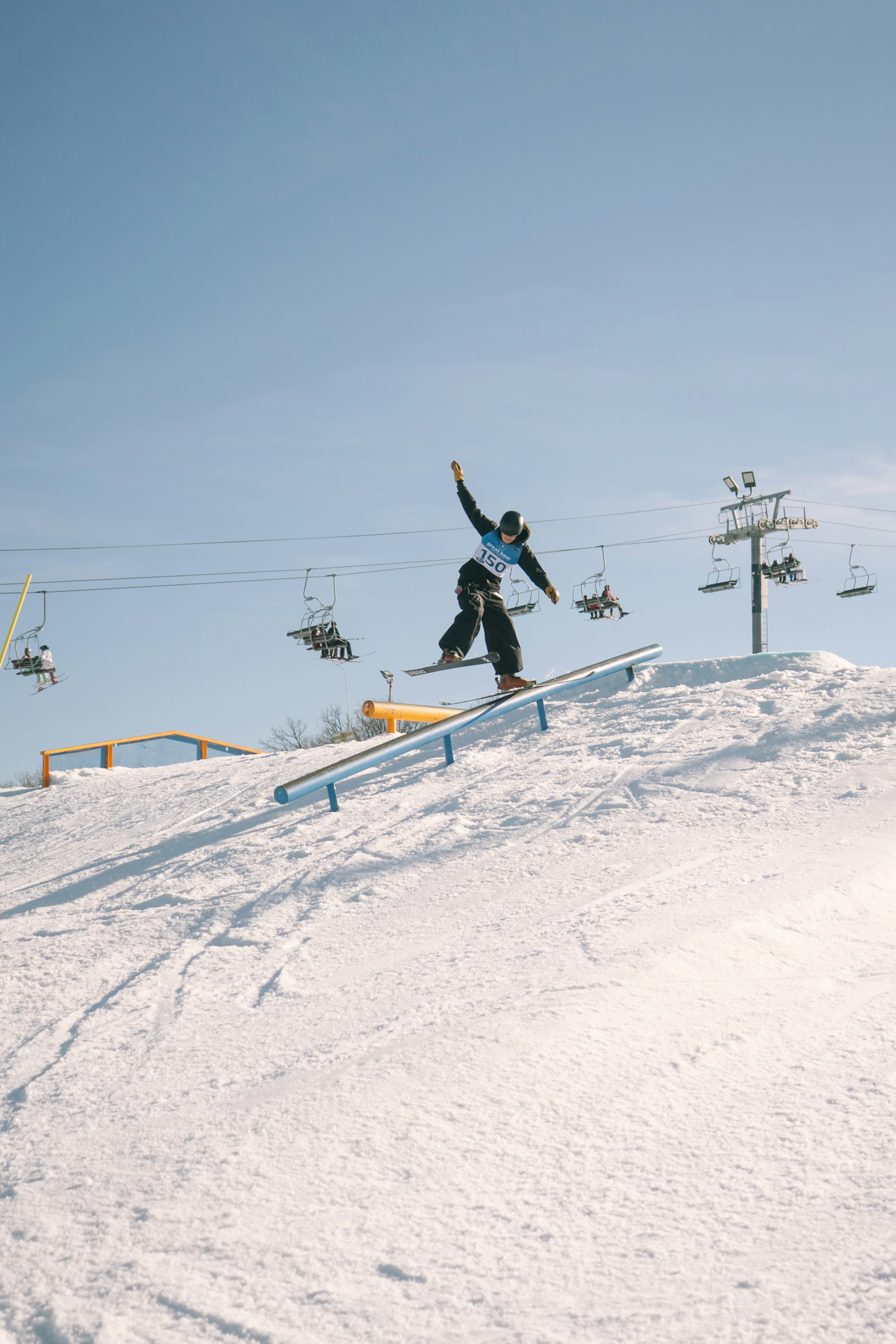 Snowboarder in mid-air over a snow-angled rail under clear blue sky