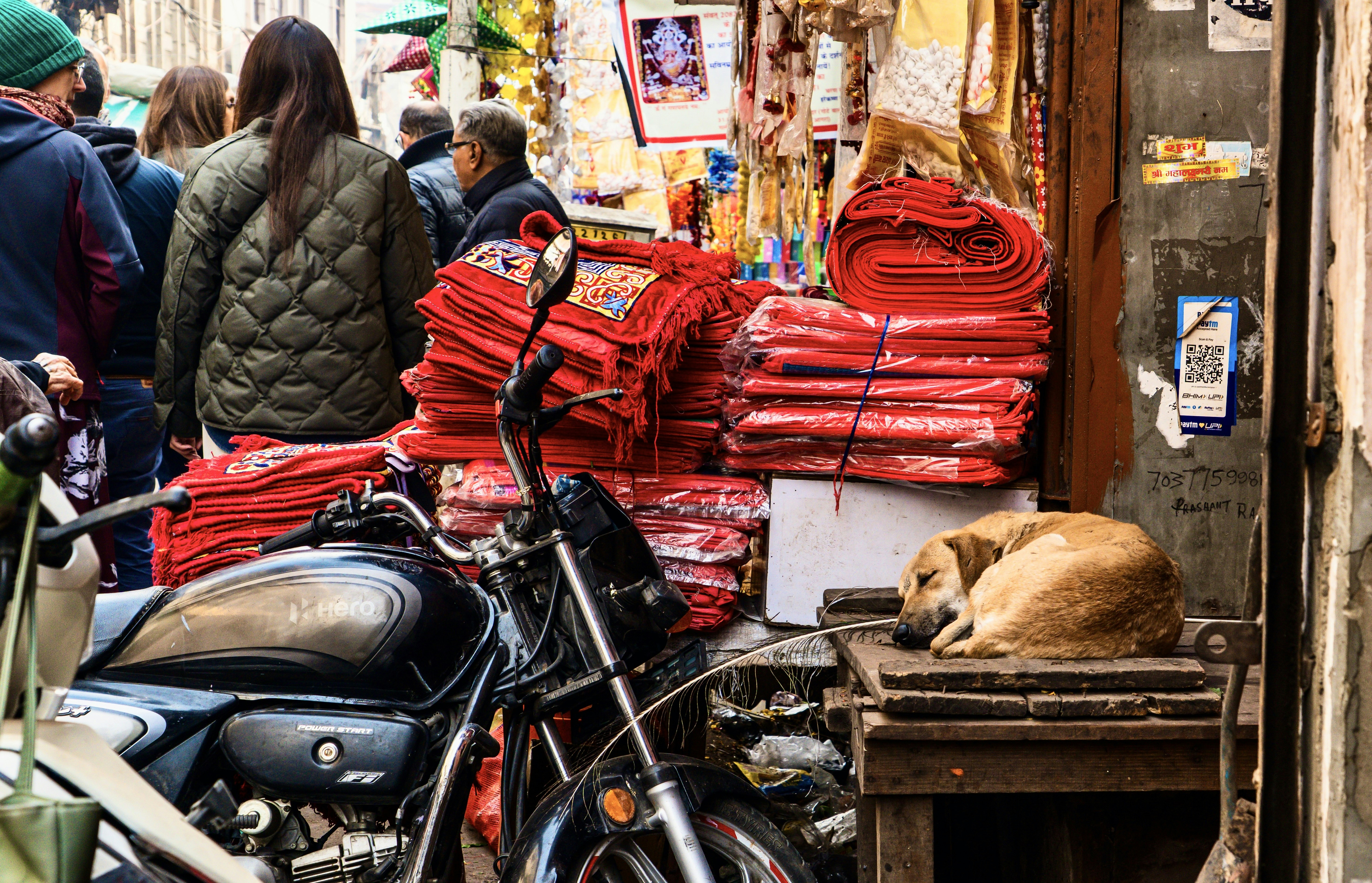 Red Textile Stacks and a Resting Dog in a Bustling Market Alley