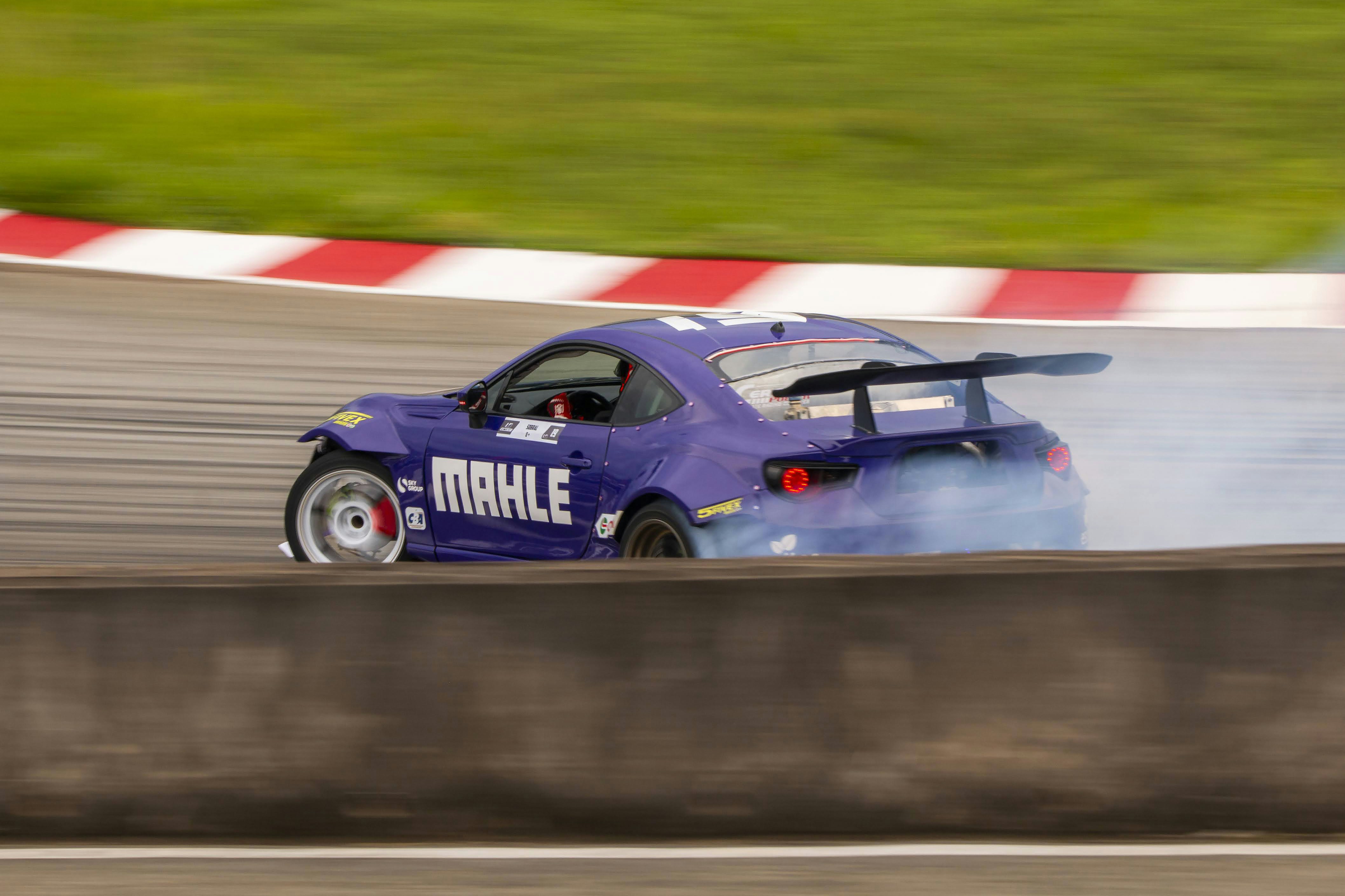 Blue race car in mid-drift along track with tire smoke