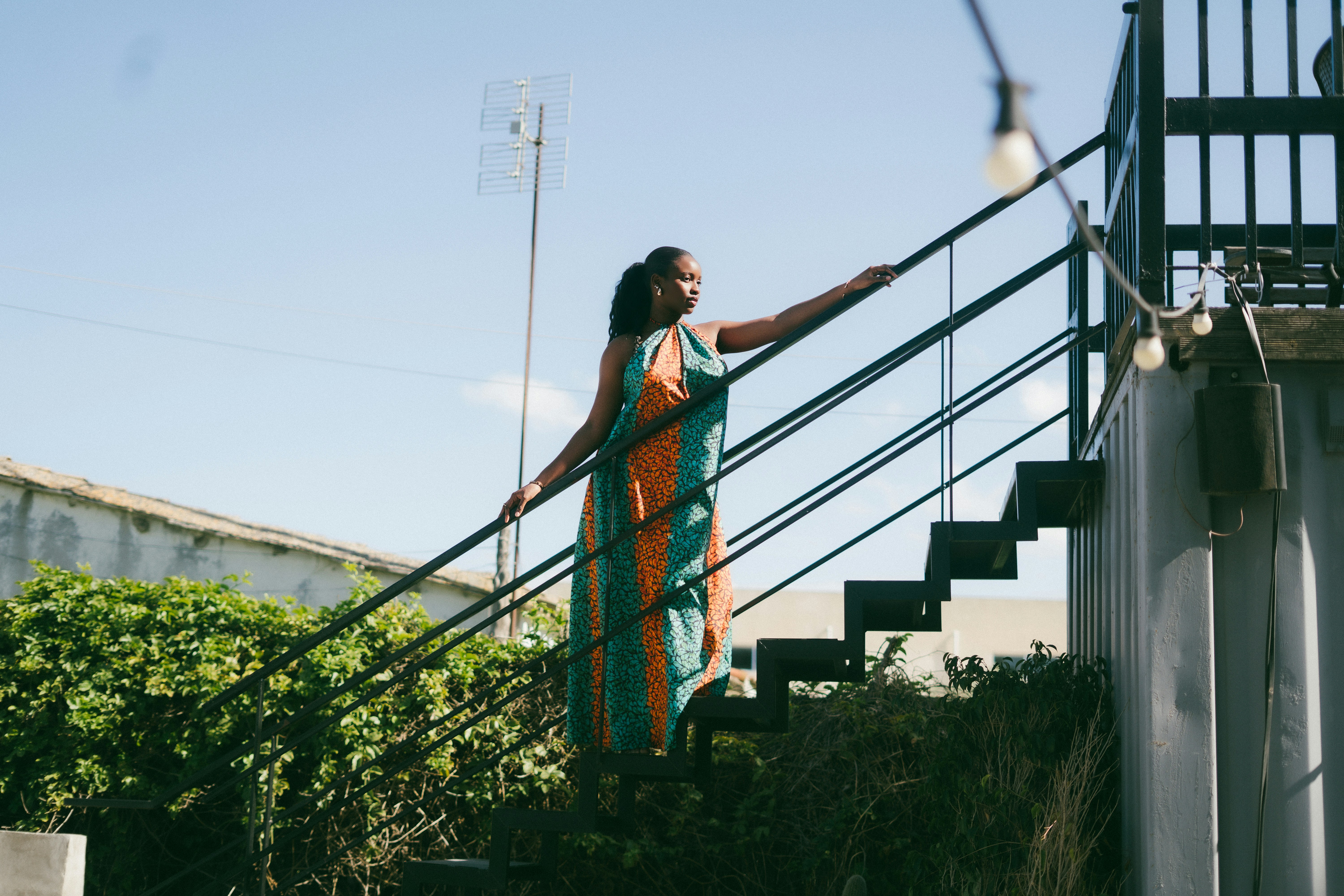 Escalating ascent: a woman in a vibrant dress climbs a sunlit outdoor staircase