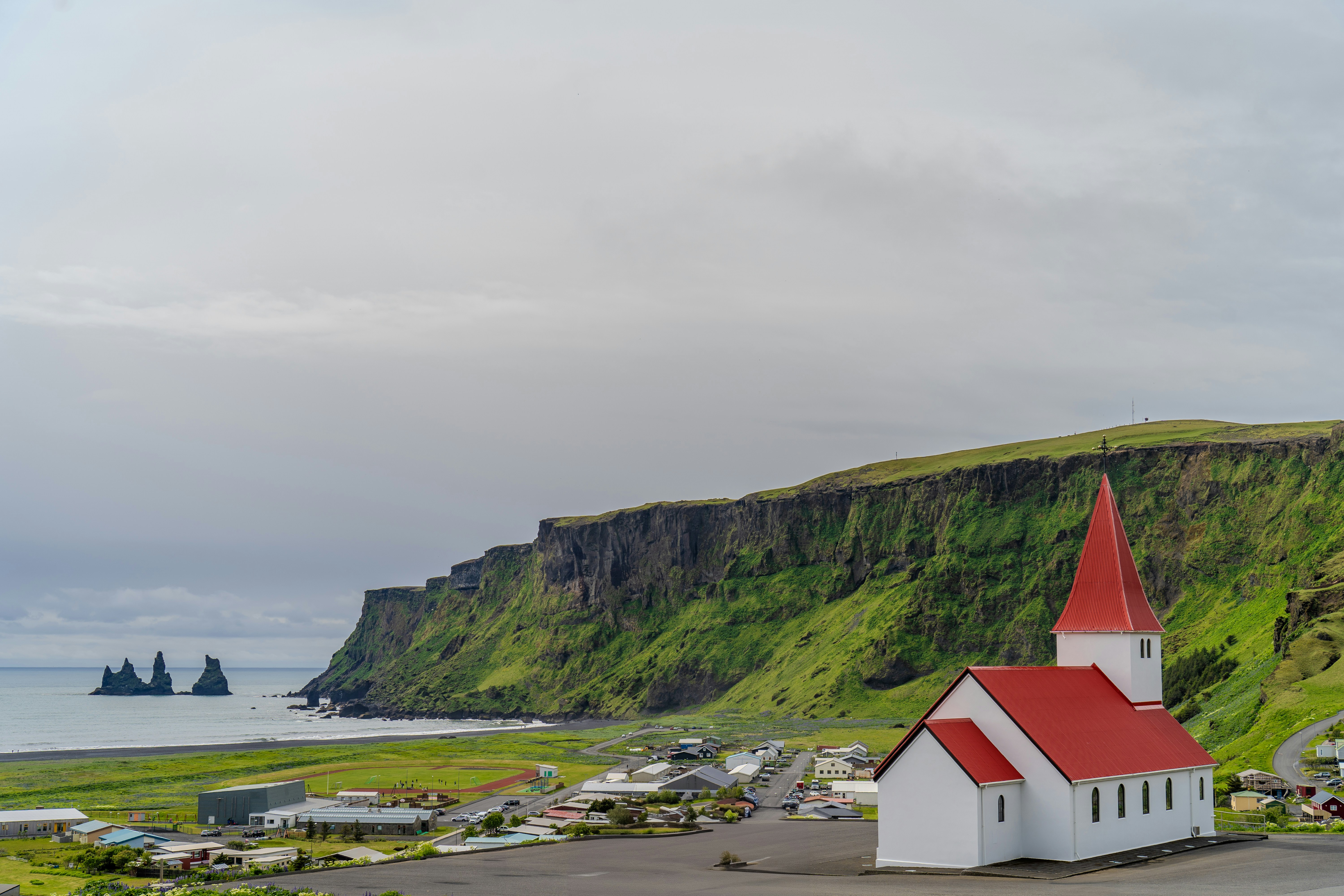 Red-roofed church at the edge of a cliff beside a quiet coastal village