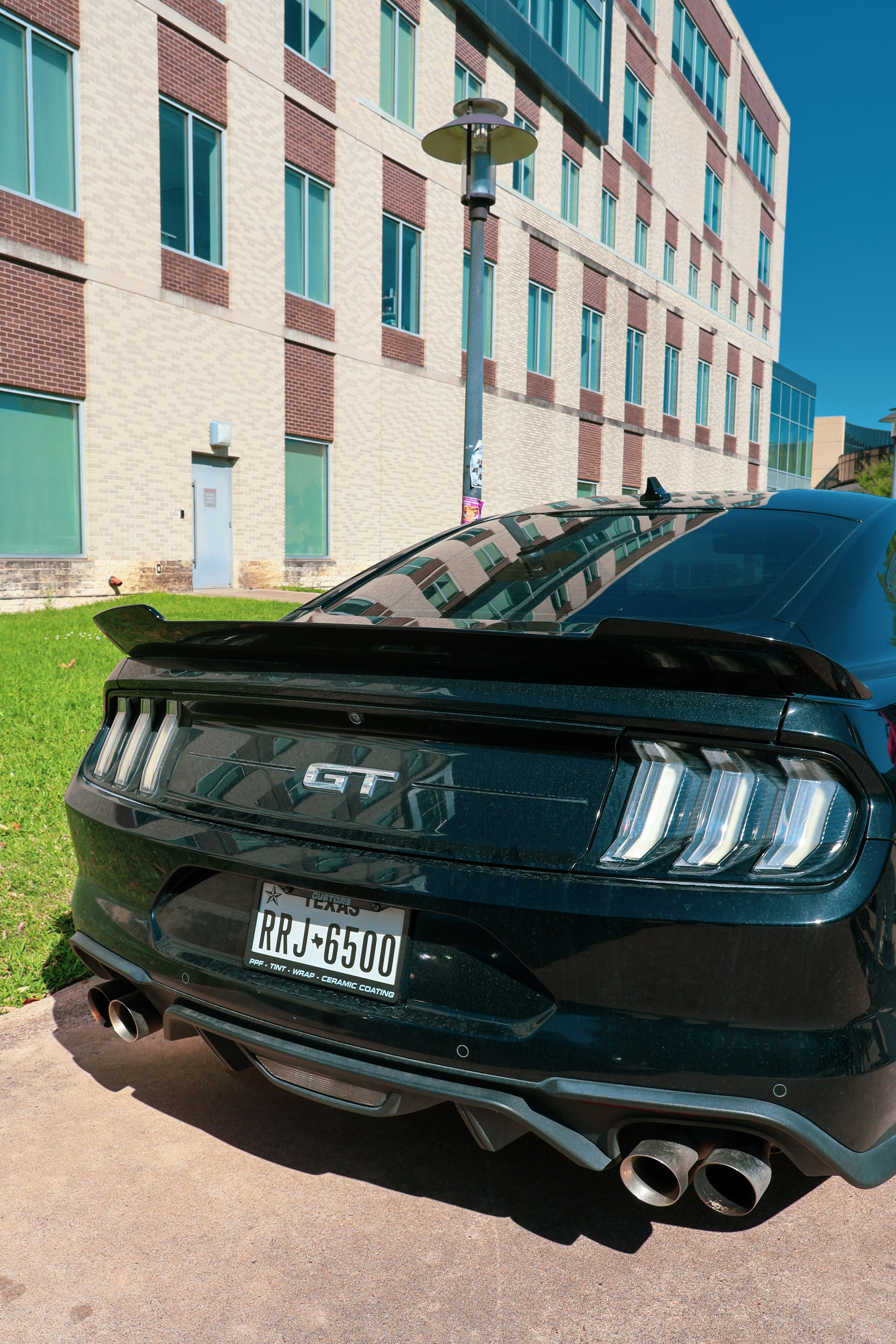Rear-Quater Drive: A Black GT Stands Bold Against a Modern Campus Facade