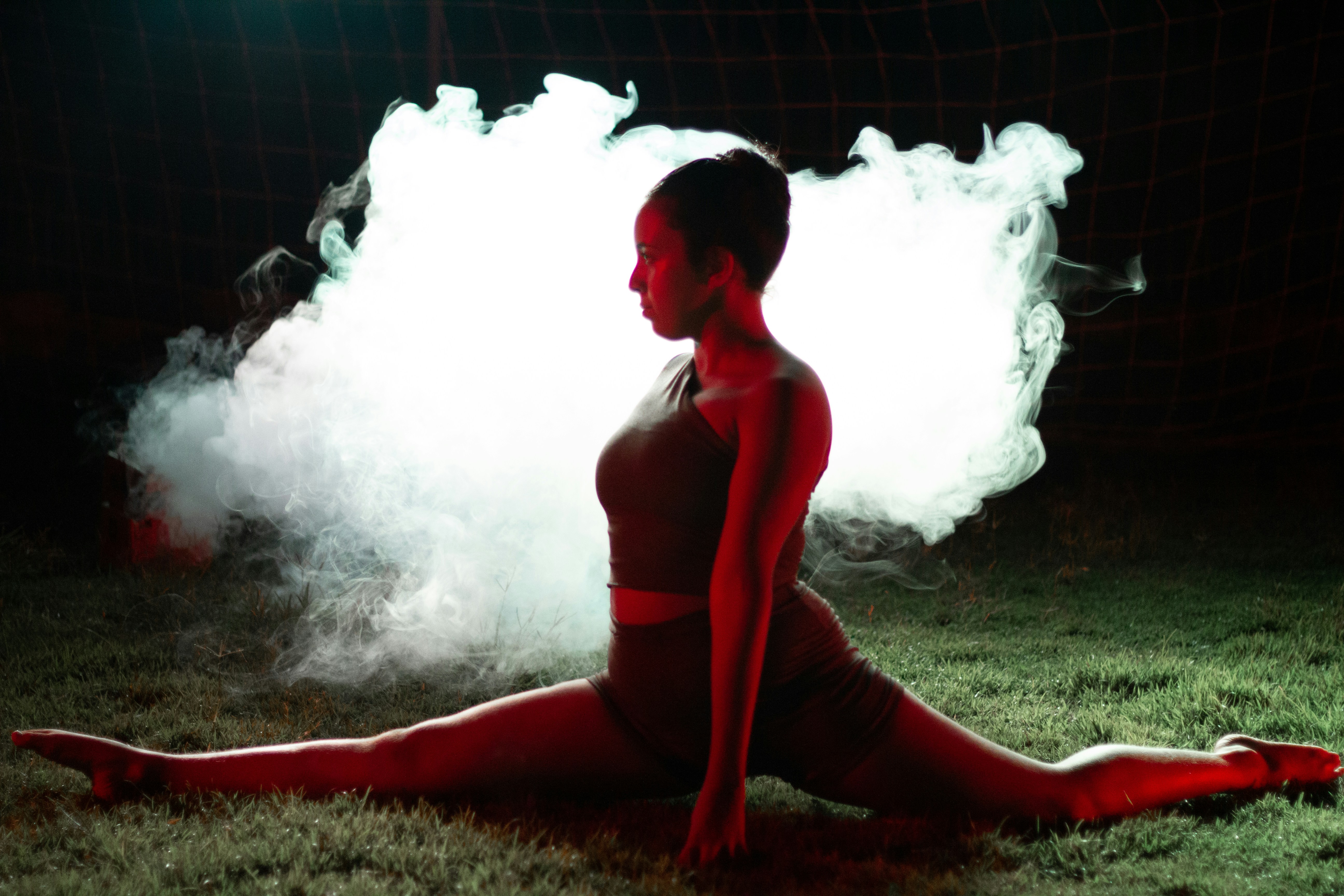 Red-lit Silhouette in Smoke: Split-Leg Pose on Night Grass