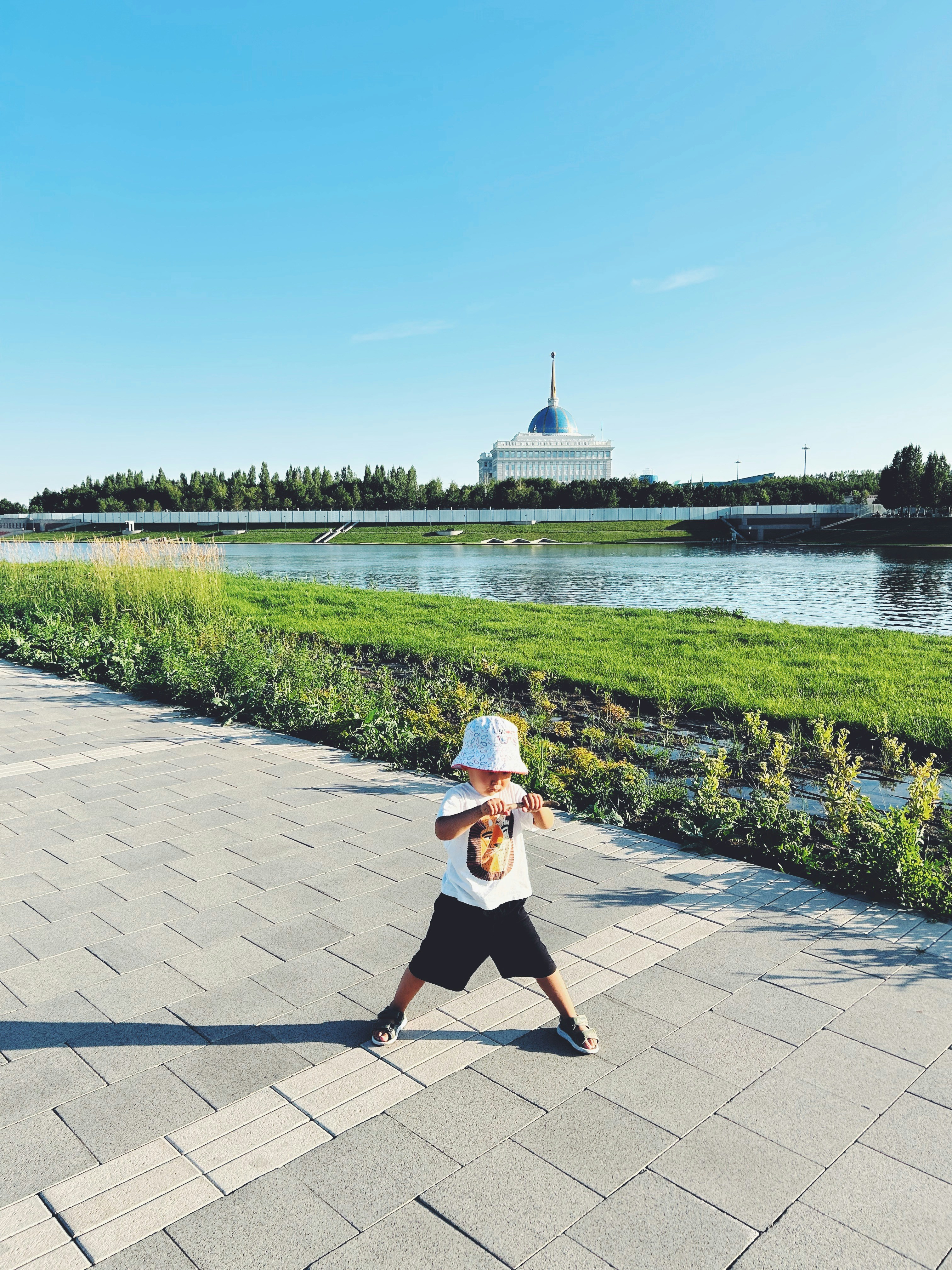 Child with white hat center-stage on sunlit riverside promenade