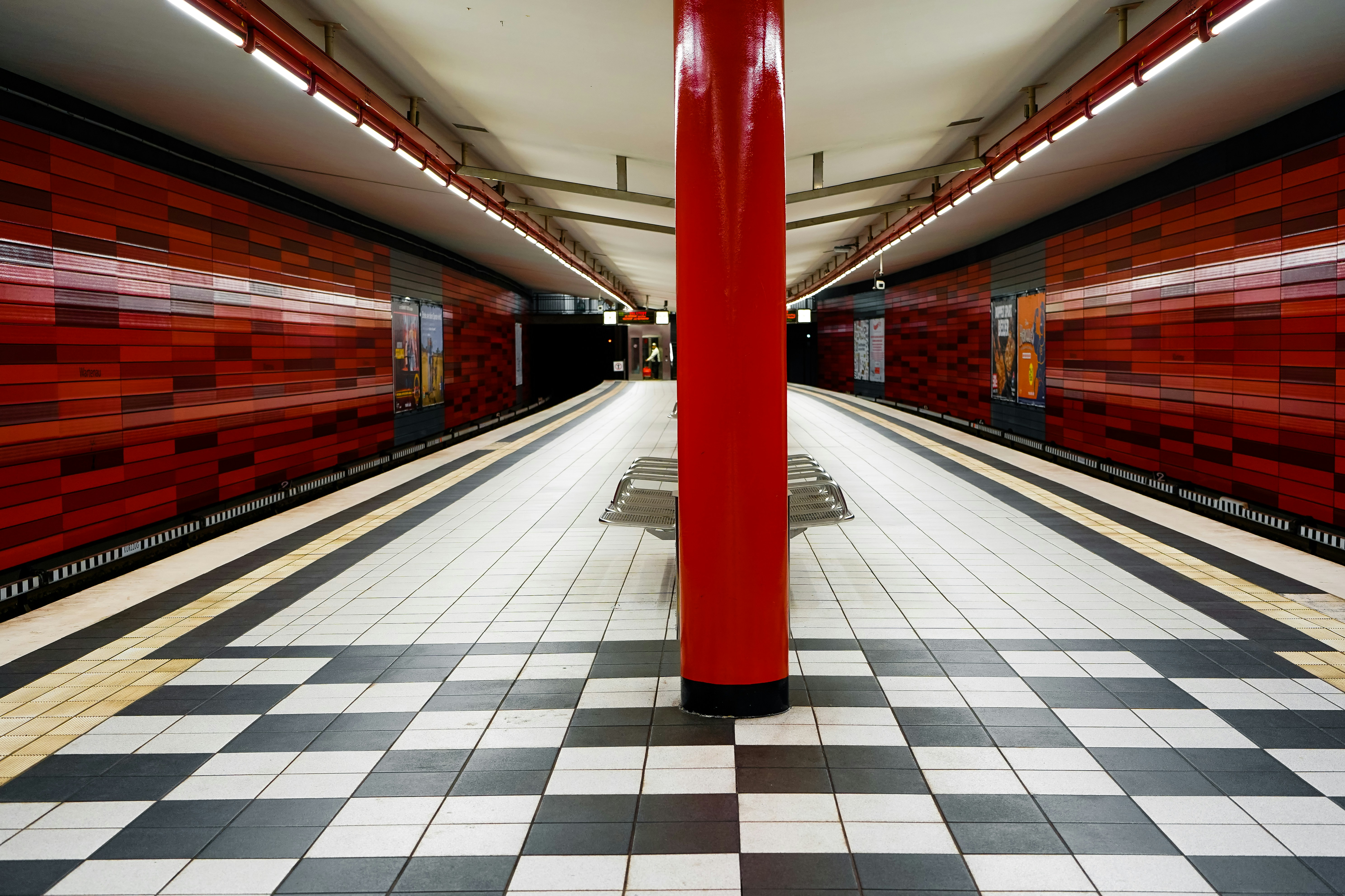 A lone column centers a checkered transit hall, stretching into a red-lit corridor