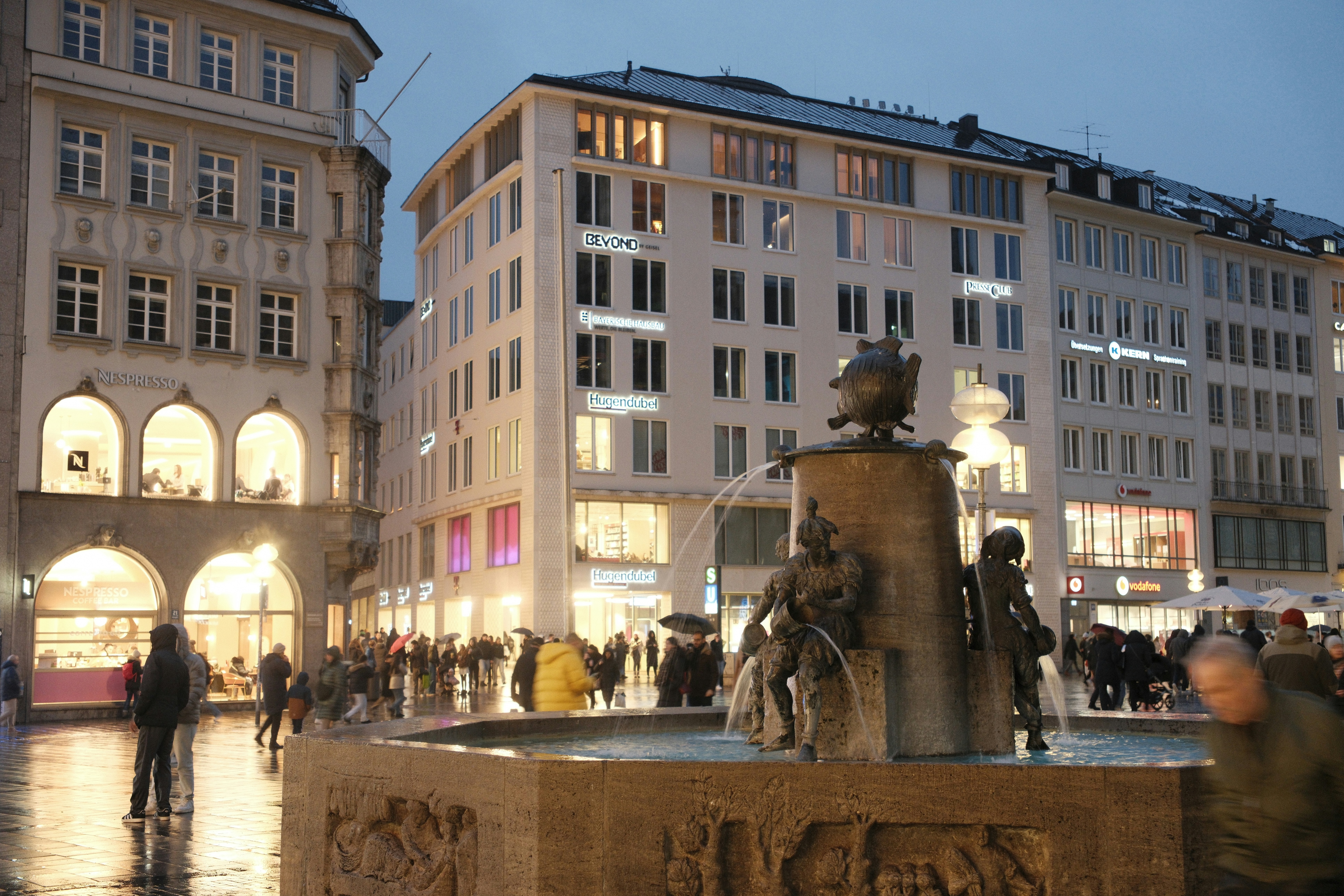 Night Piazza: A Bustling Fountain Surrounded by Warm Shopfronts