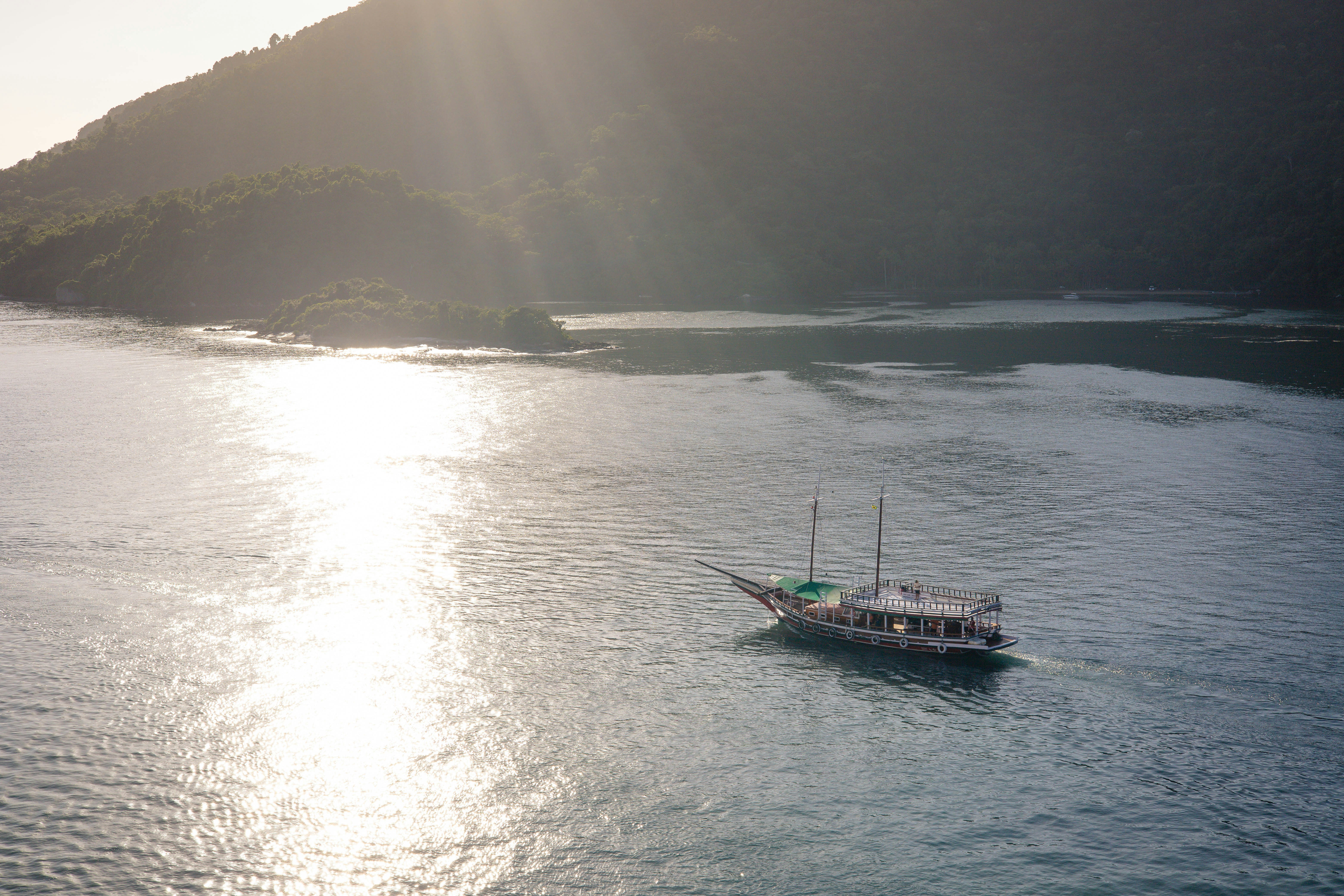 Sunlit harbor: a lone boat glides along shimmering water near a forested shoreline