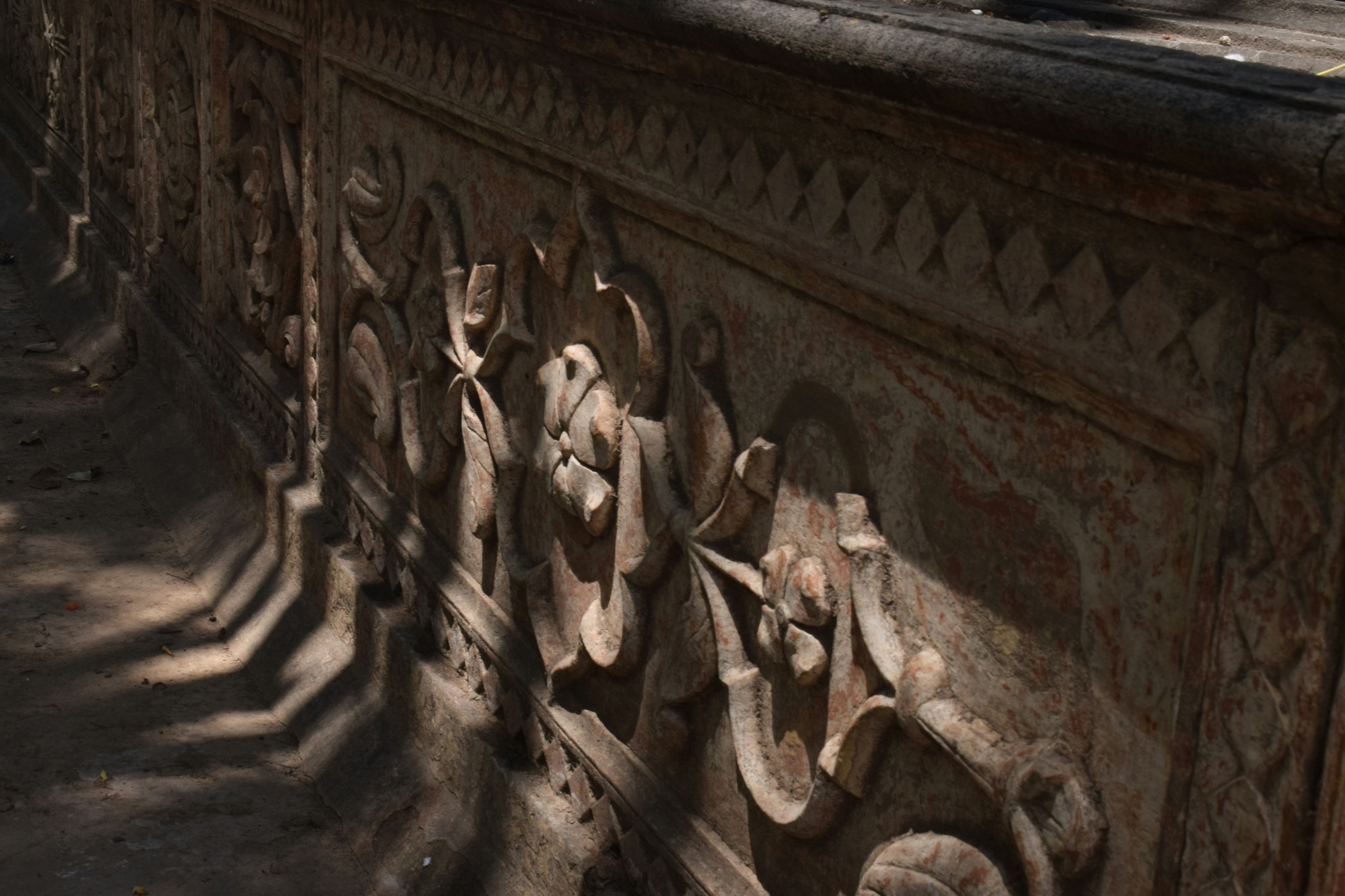 Shadowed Carvings: A Row of Weathered Floral Reliefs along Dappled Stone