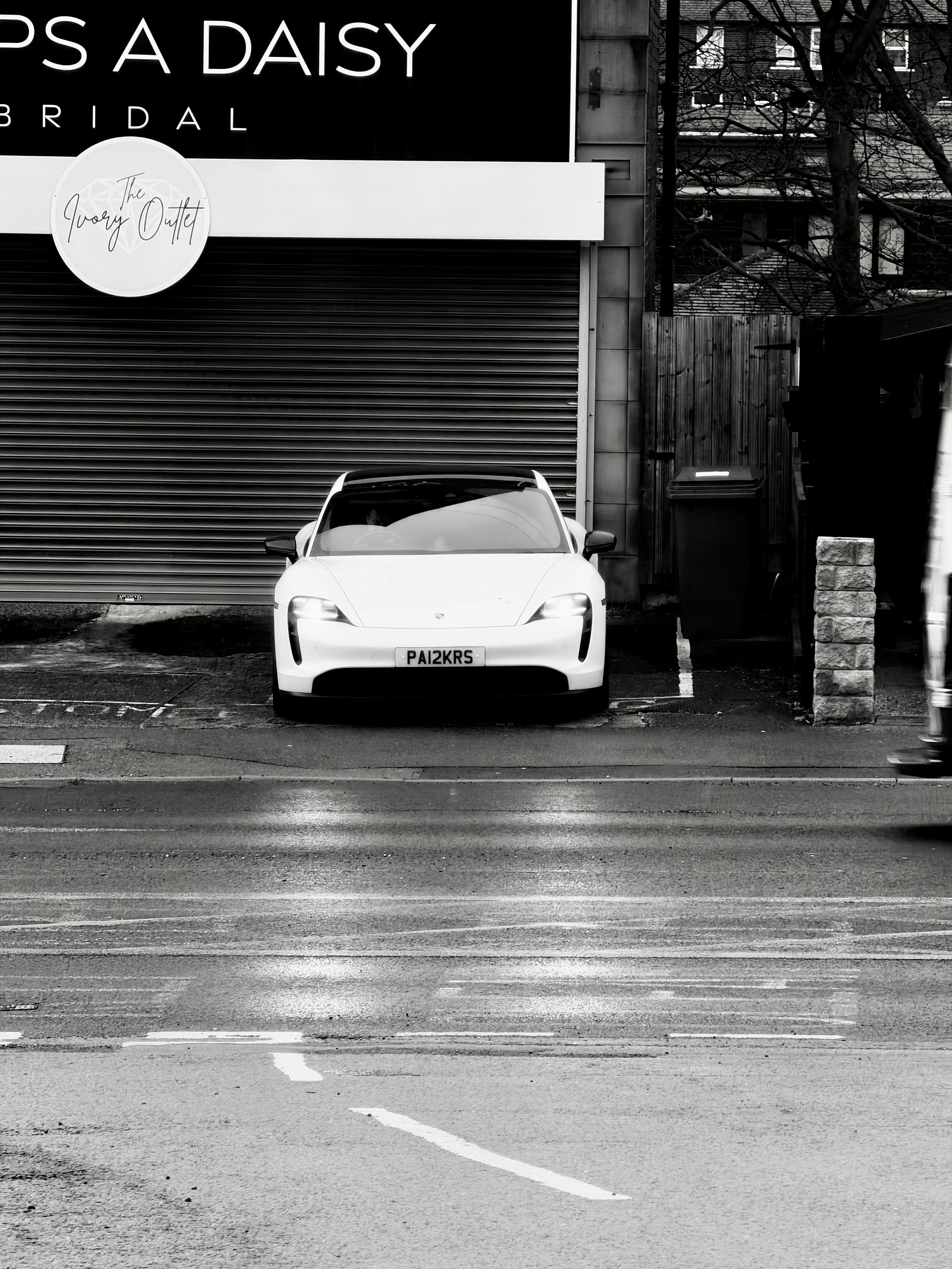 White electric car centered under a closed storefront in urban monochrome