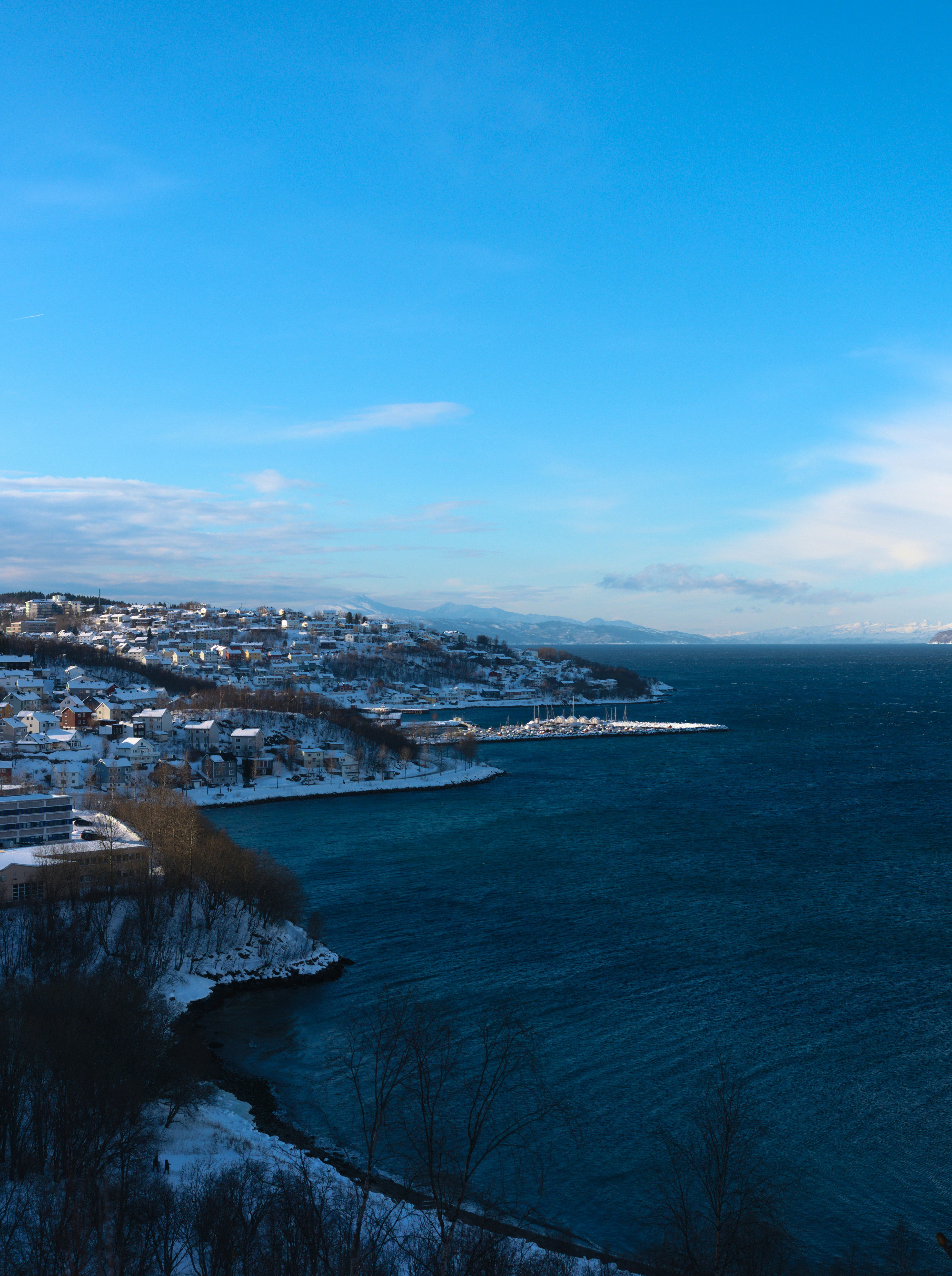 Snow-kissed coastline: village and pier hugging the blue sea under a clear sky