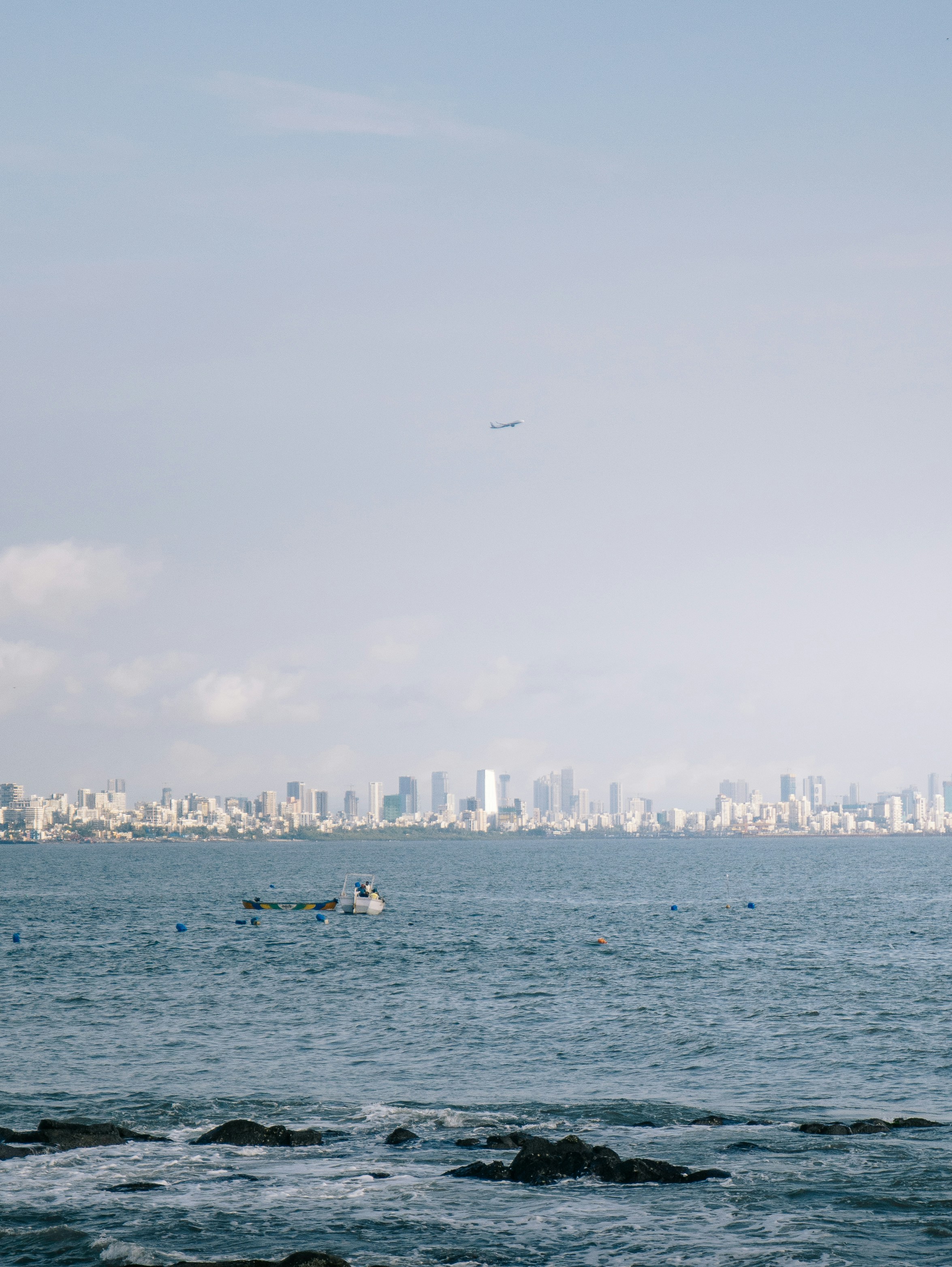 City skyline bleeds into horizon as a lone boat glides across the calm sea