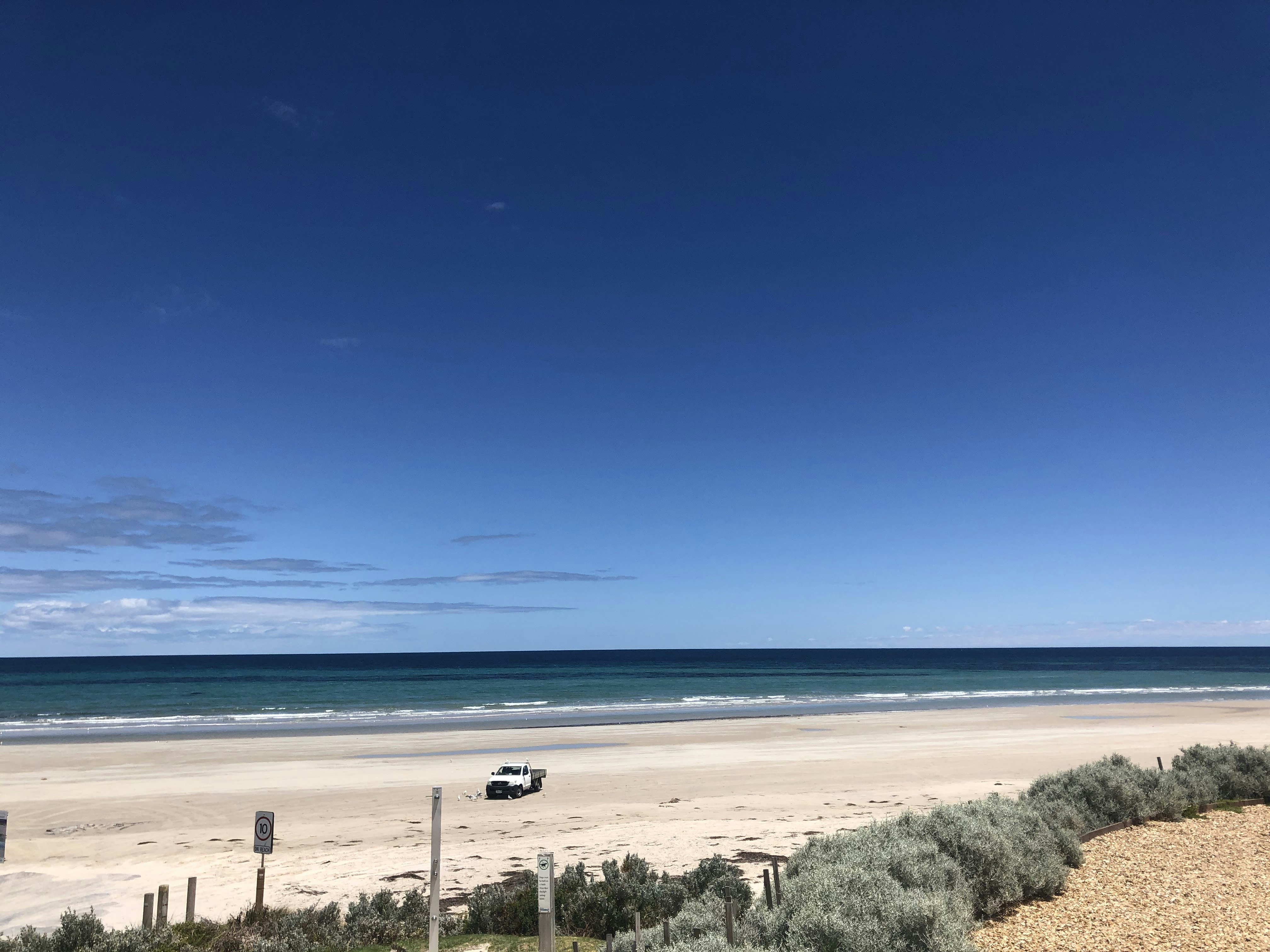 Quiet Beachfront Calm: A Lone Vehicle on the Sand by Blue Horizons