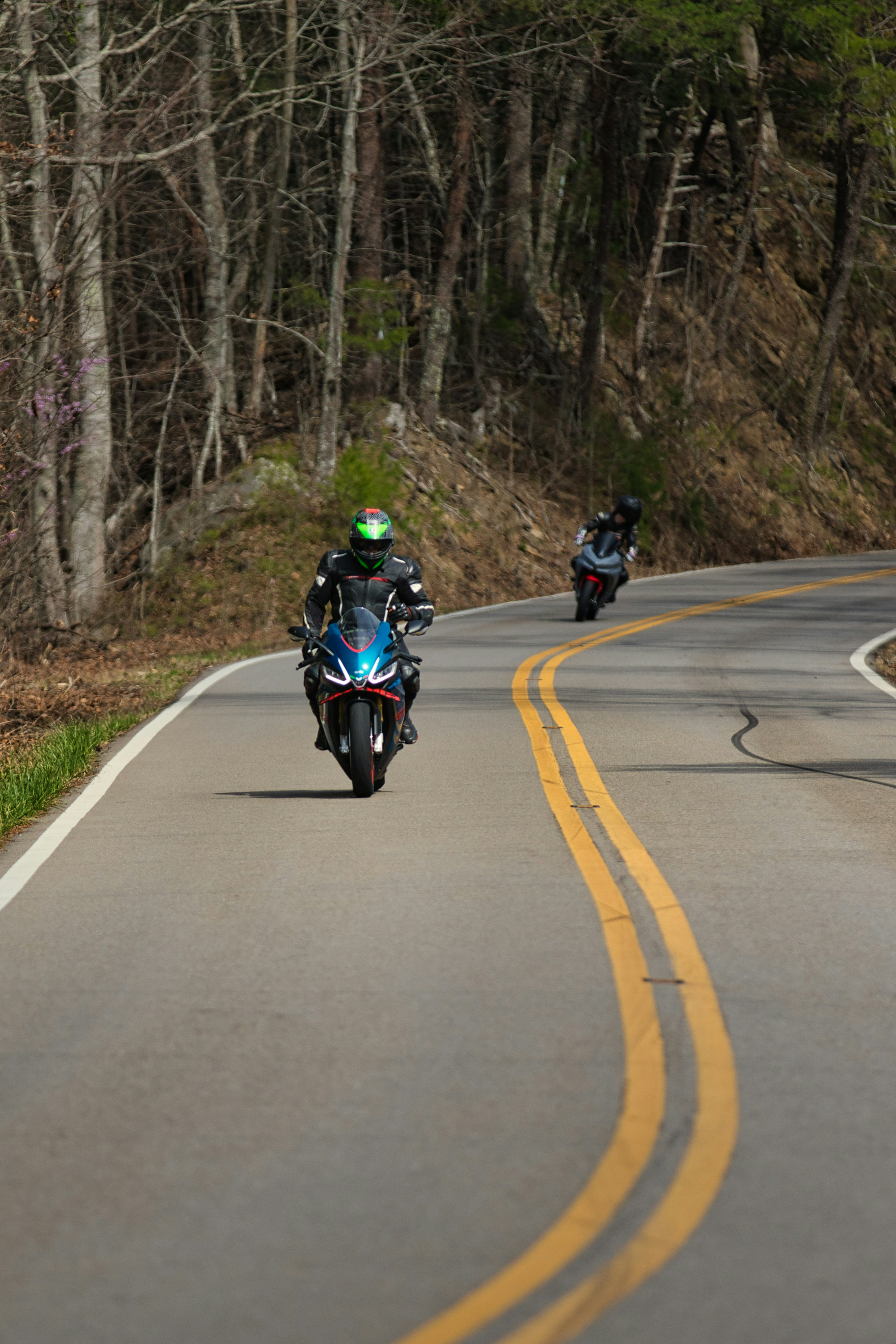 Ahead on the Curve: Neon-helmeted Rider Leads a Quiet Mountain Road