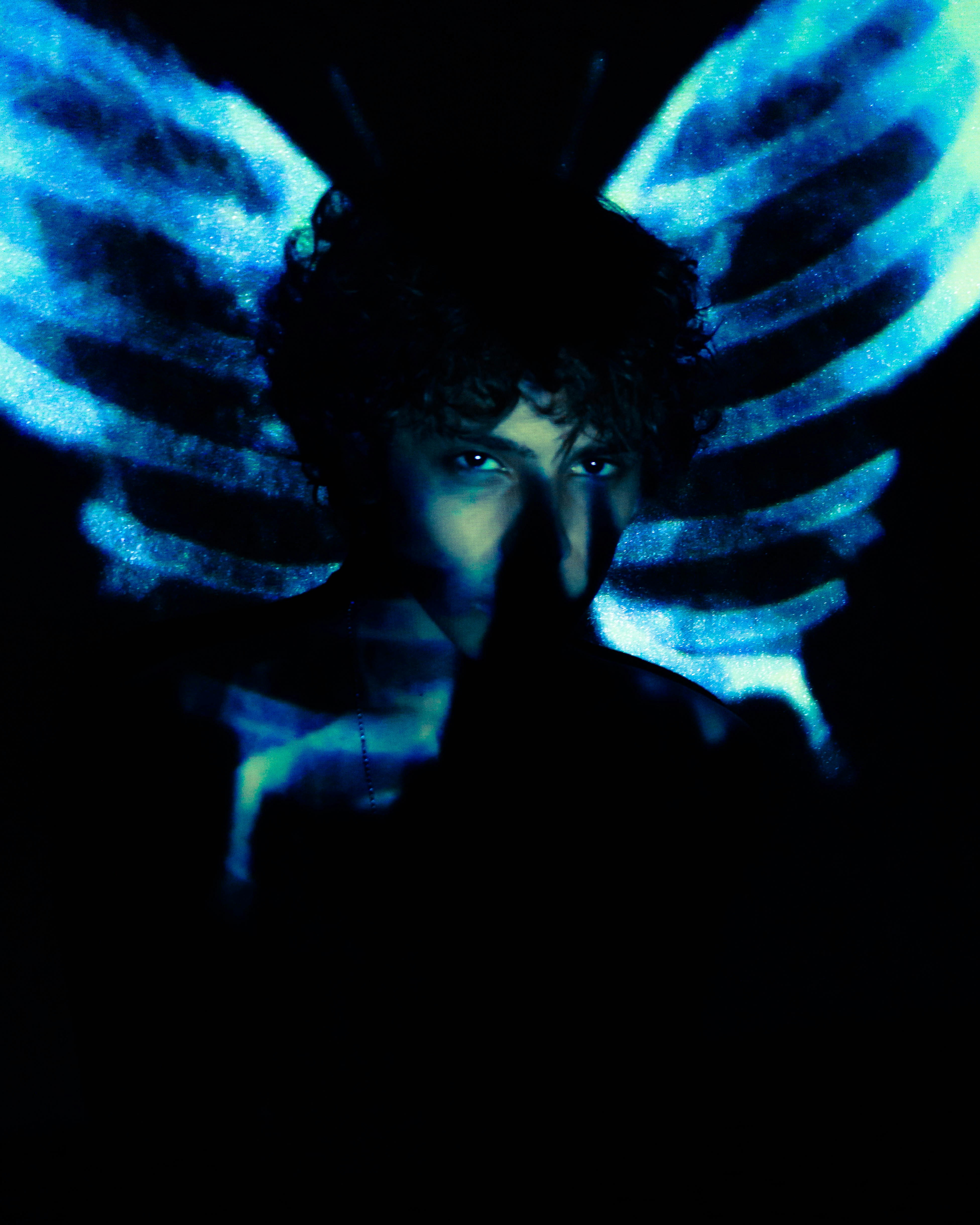 Winged silhouette: blue projection frames a piercing gaze