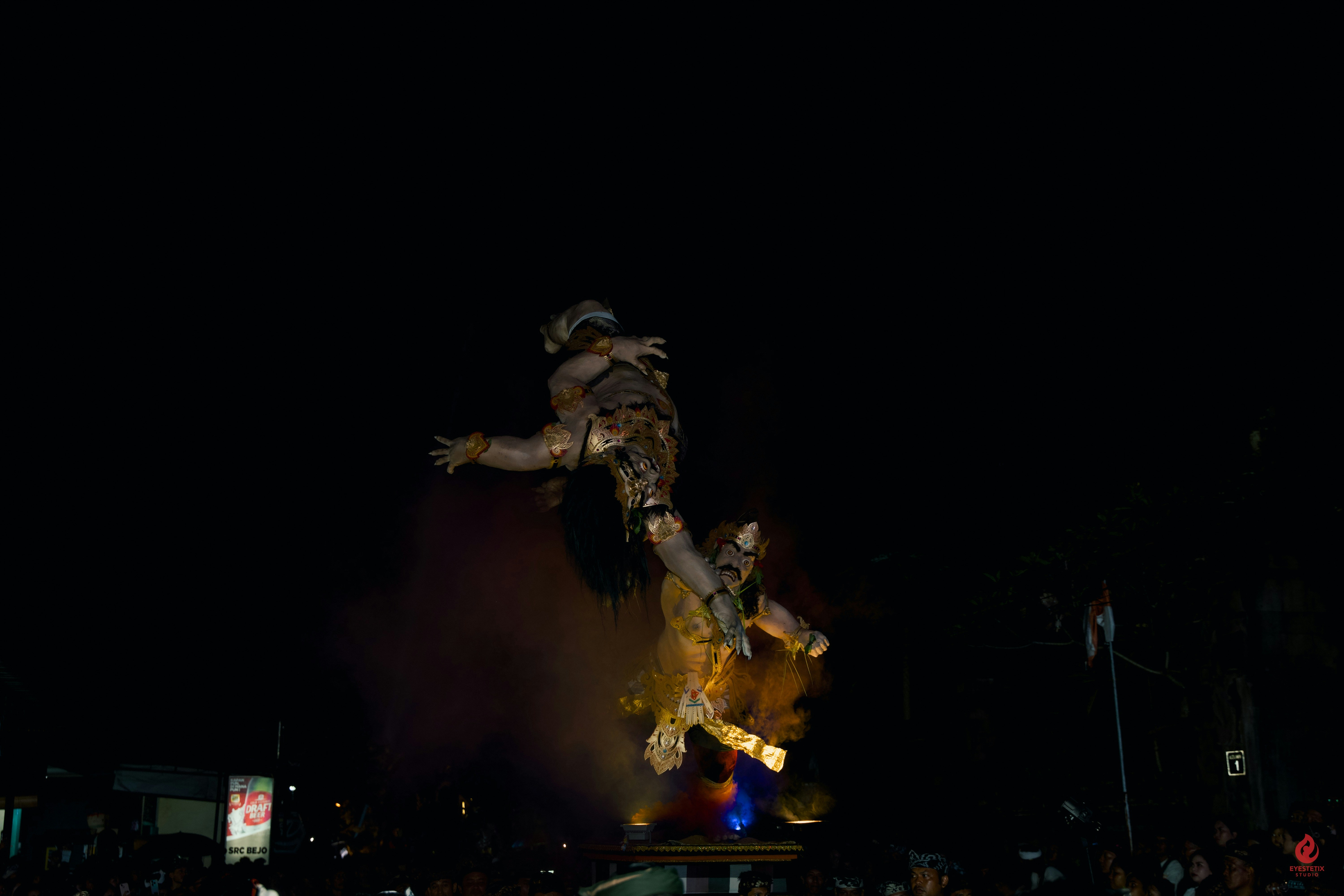 Night-time Druidic Jump: Fiery Figure Rises Over a Crowded Street