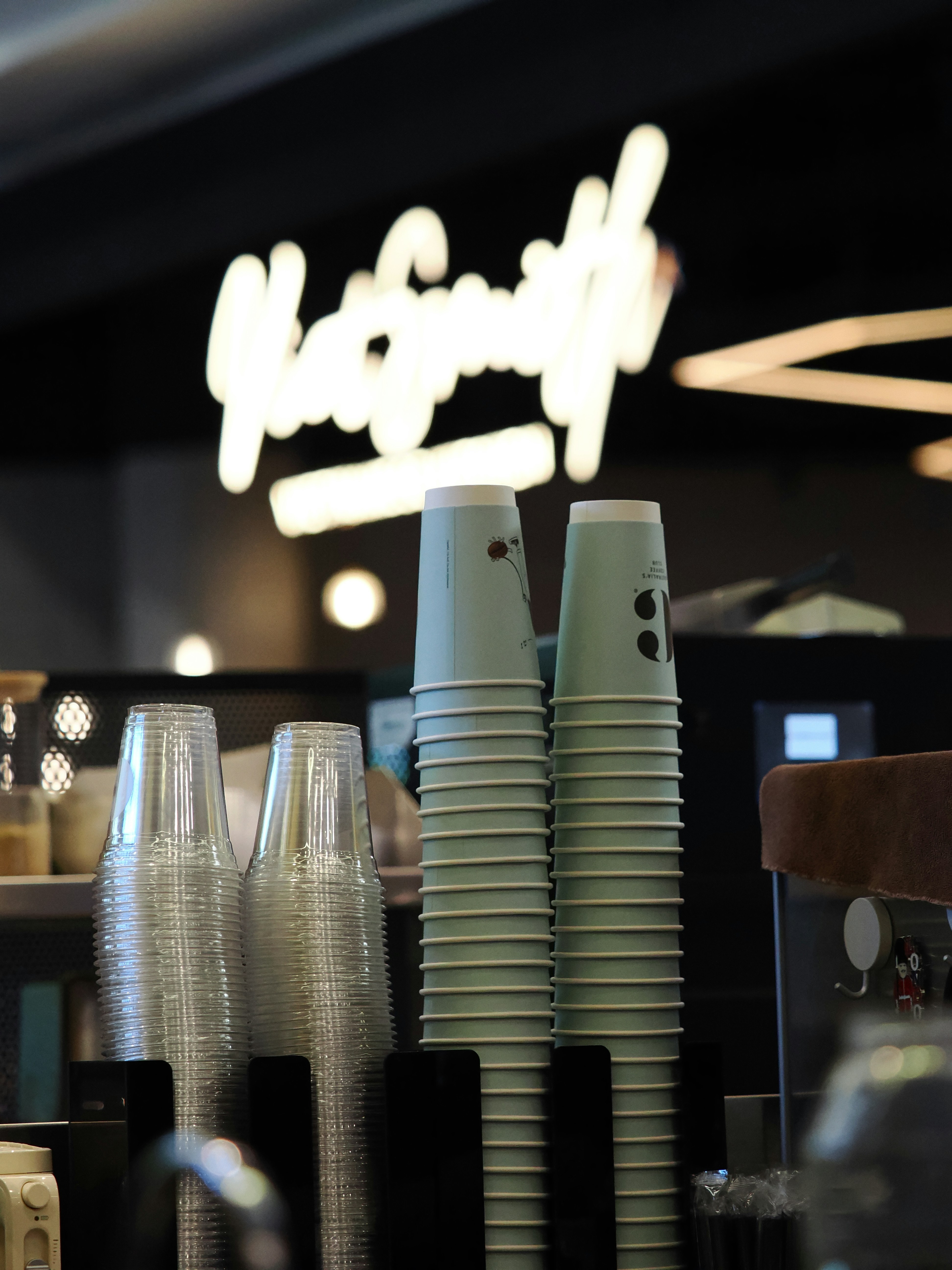 Stacked cups and neon glow: a quiet barista scene under blurred marquee lights