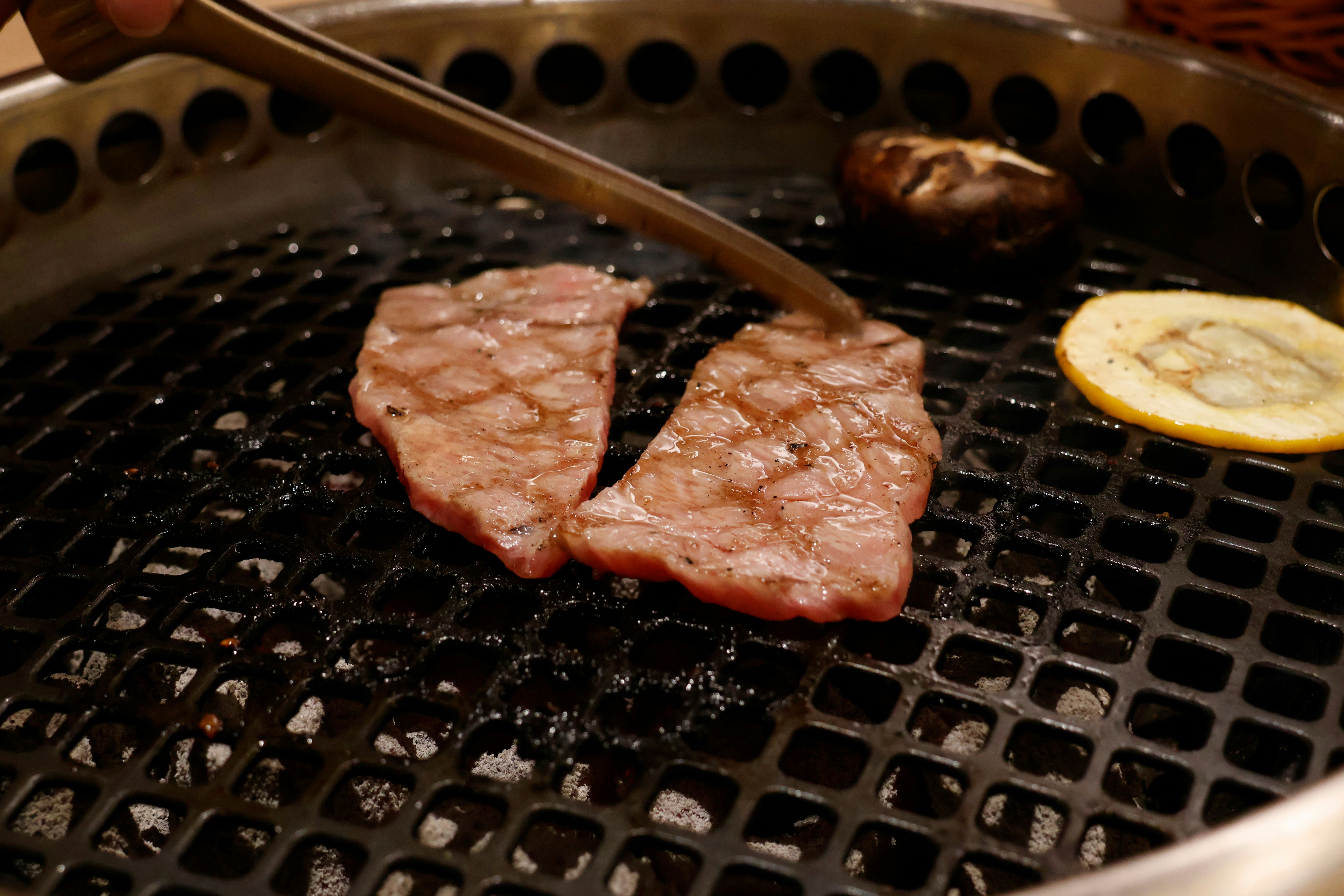Sizzling two slices on a grill: close-up of searing beef with lemon slice and mushroom