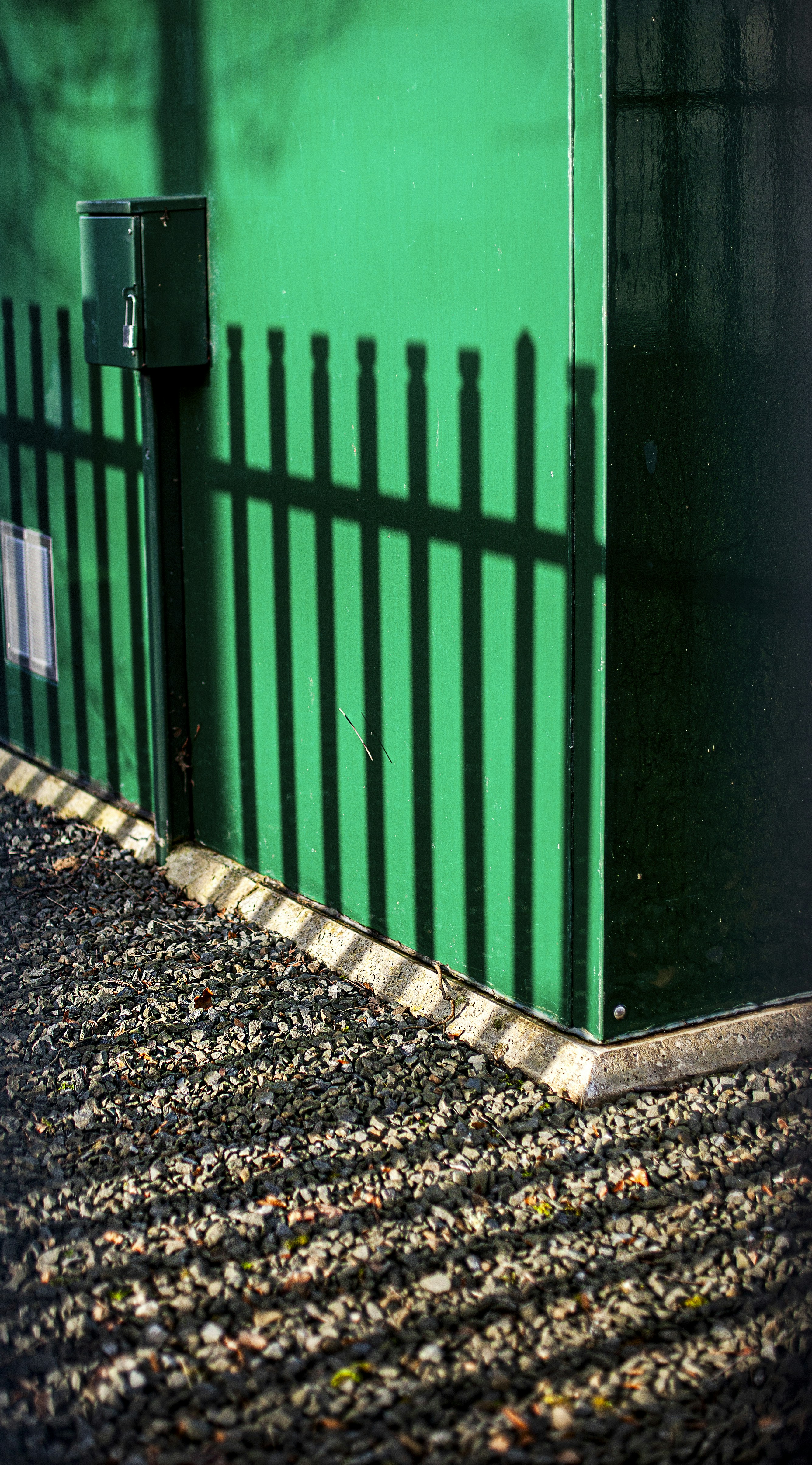 Green Facade, Shadowed Fence: A Quiet Corner of Metal and Gravel