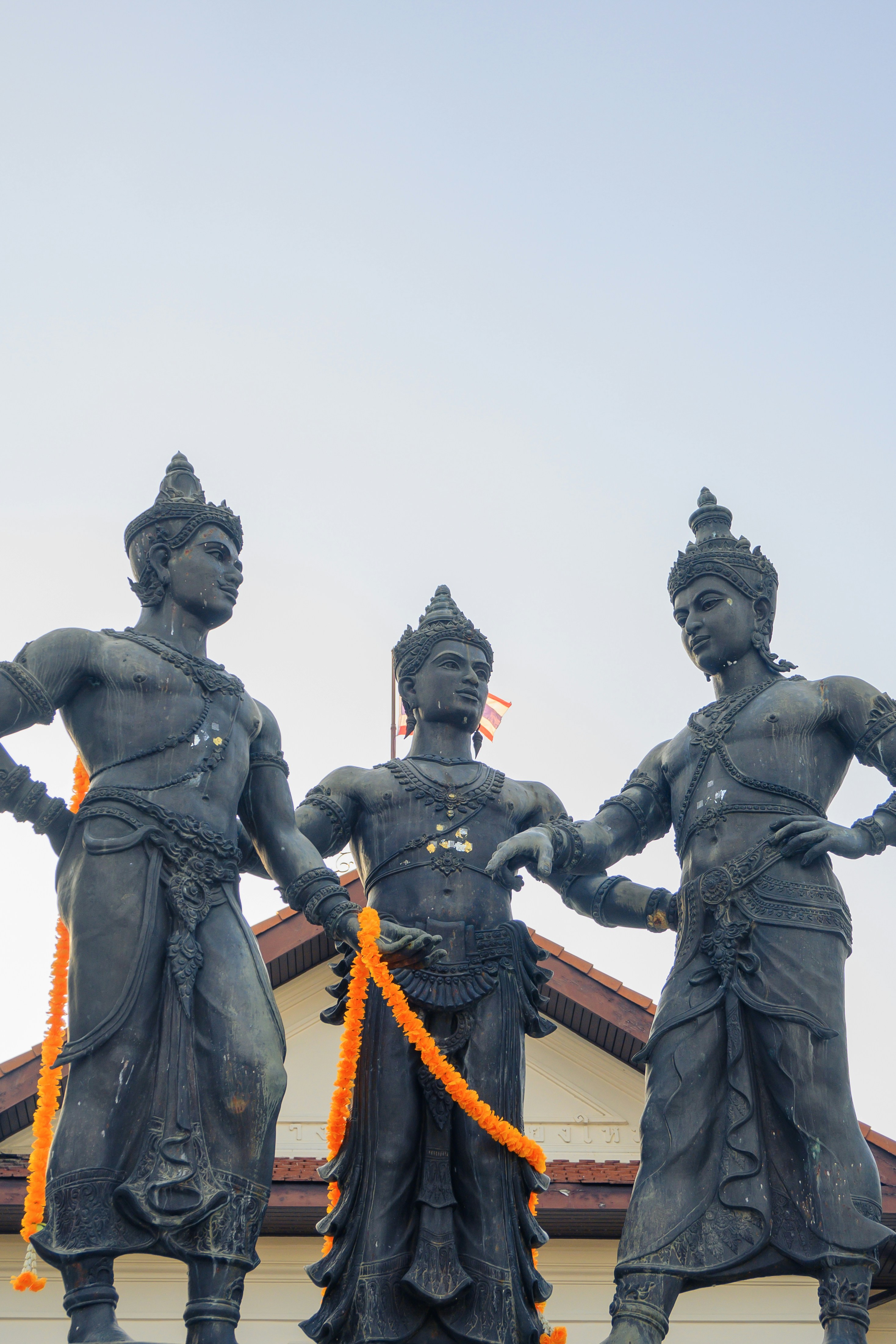 Three Guardian Statues with Orange Garlands Under a Clear Sky