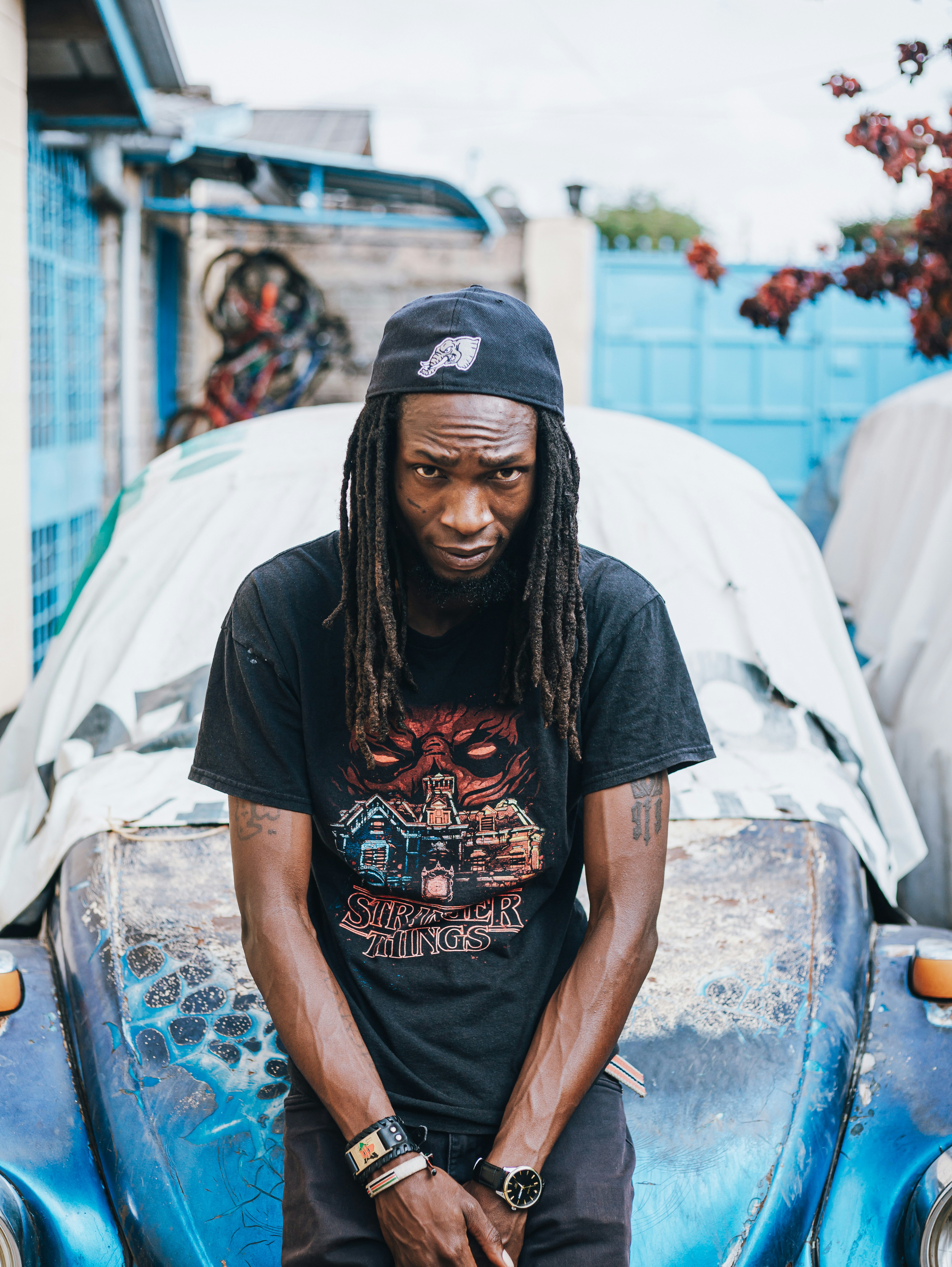 Portrait in the Yard: A Quiet Rebel Stands Before a Weathered Blue Car