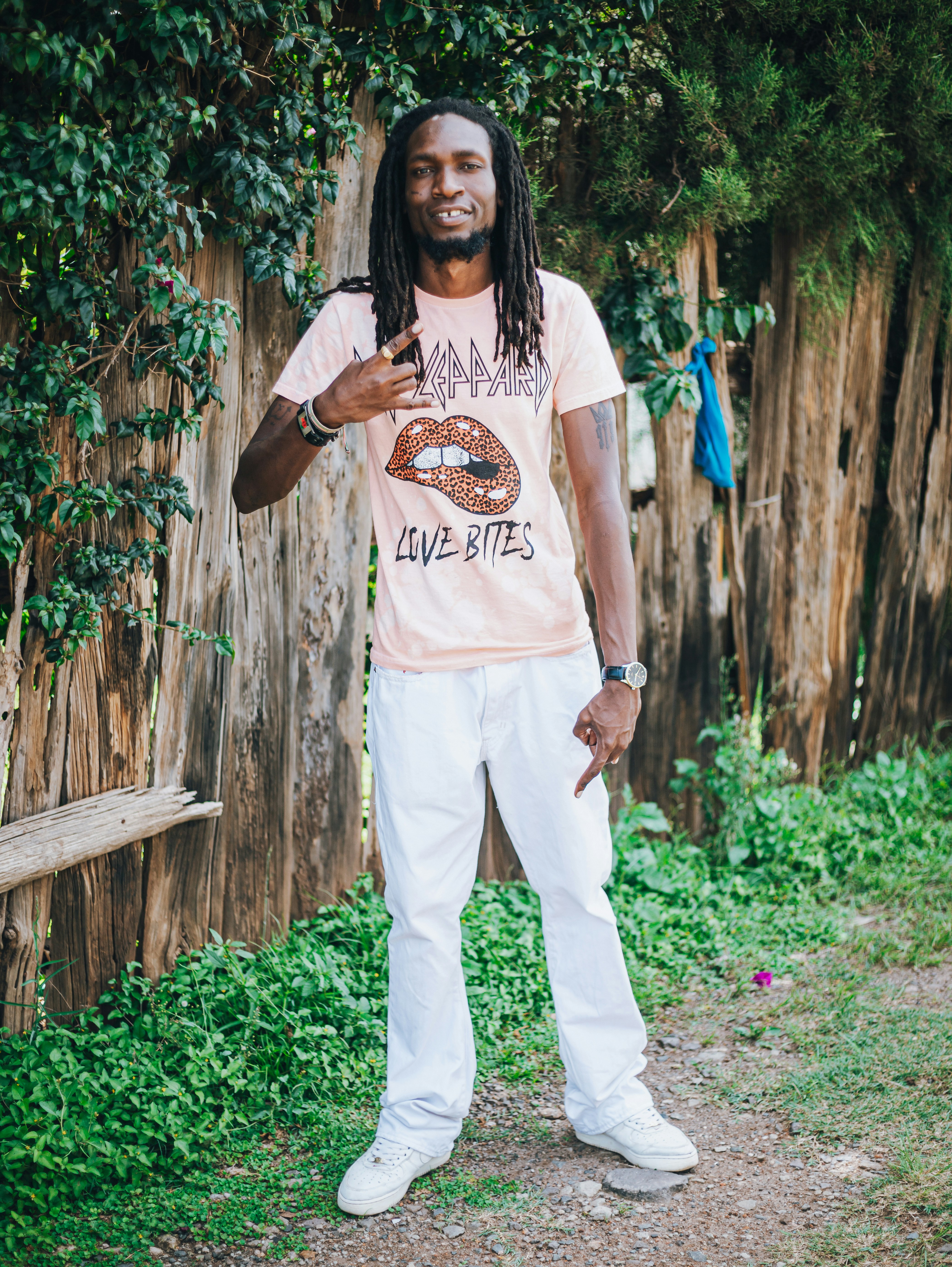 Portrait of Confidence: A Man in Peach Tee Stands Tall Along a Weathered Fence