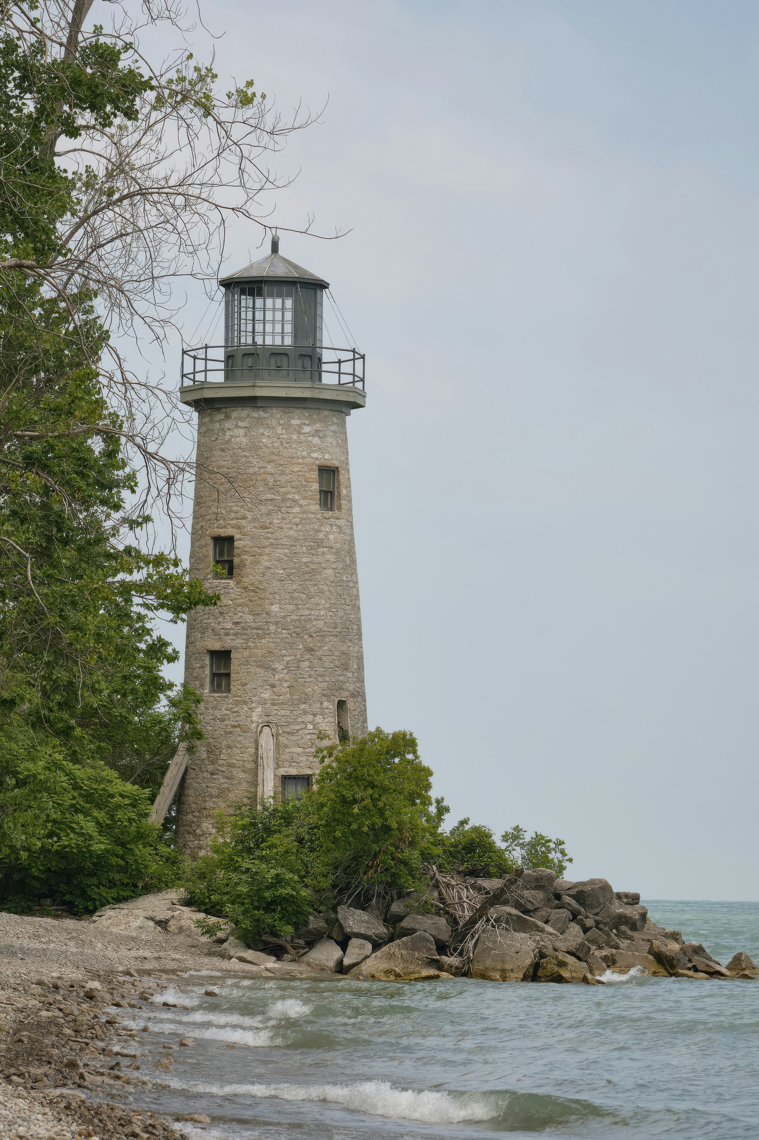 Stone Sentinel by the Sea: A Quiet Lighthouse Bordered by Greenery