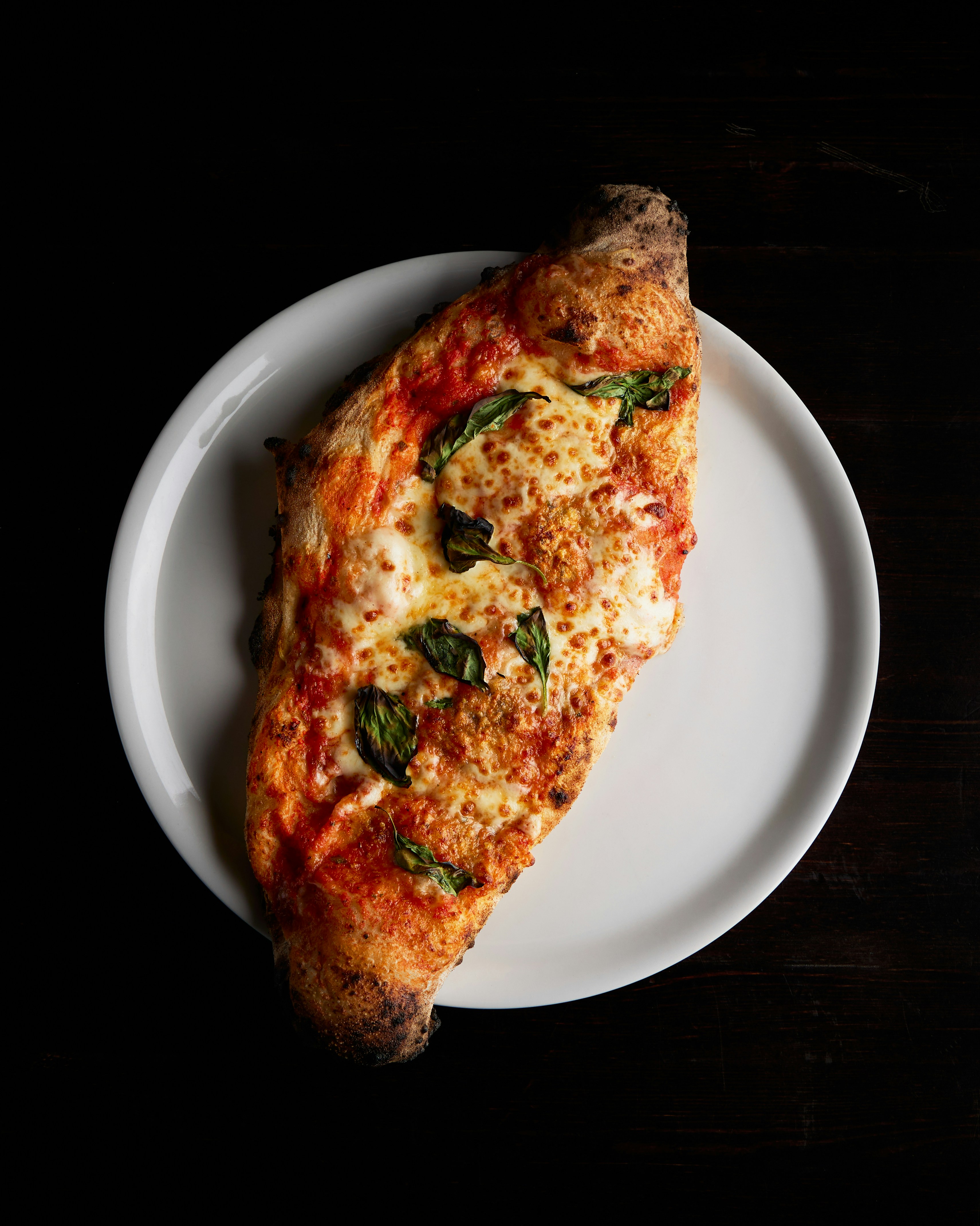 Savory prow: a slice of basil-kissed pizza perched on a white plate