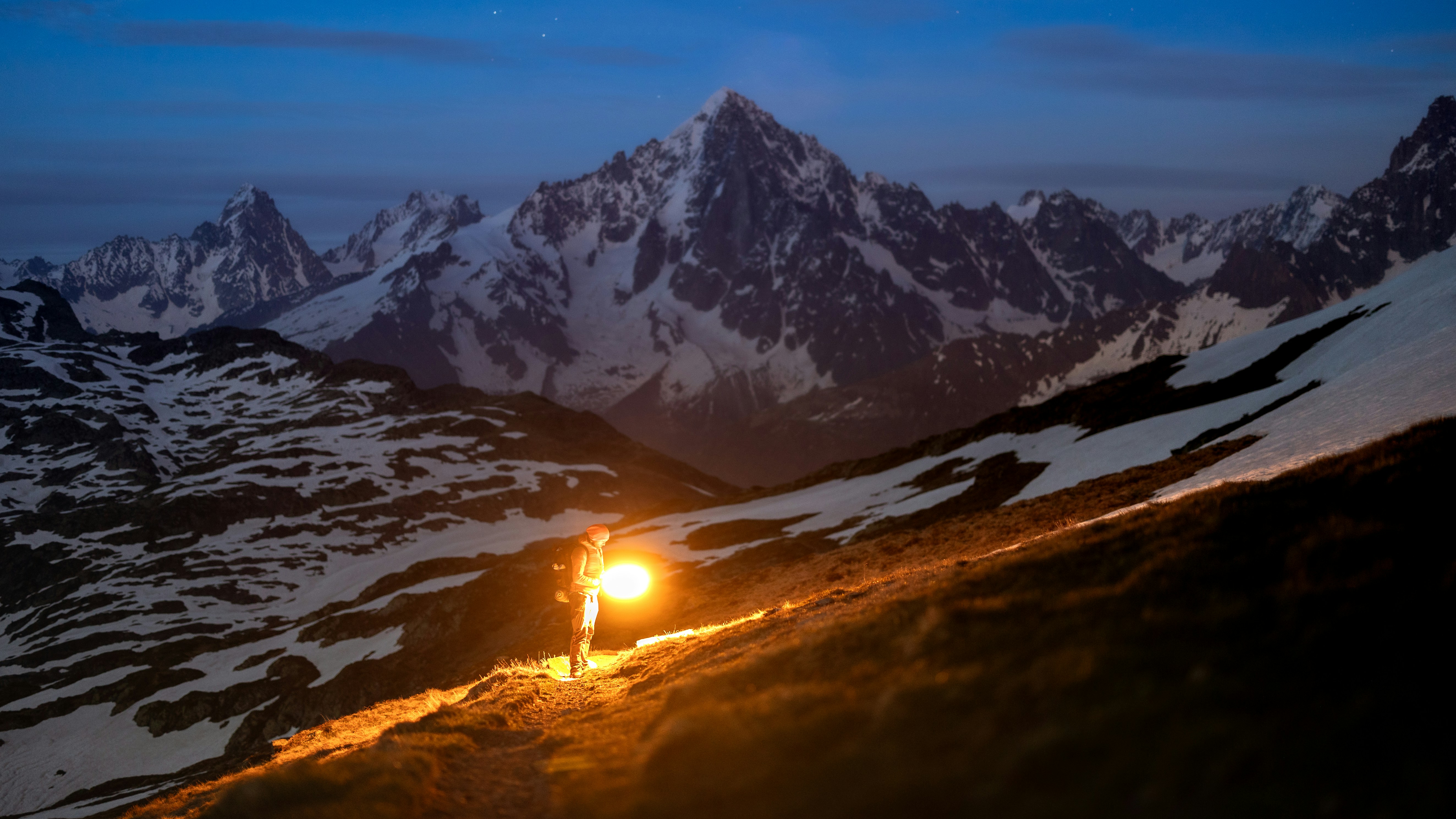 Lone Lantern: Climber Illuminates a Snow-streaked Ridge at Dusk