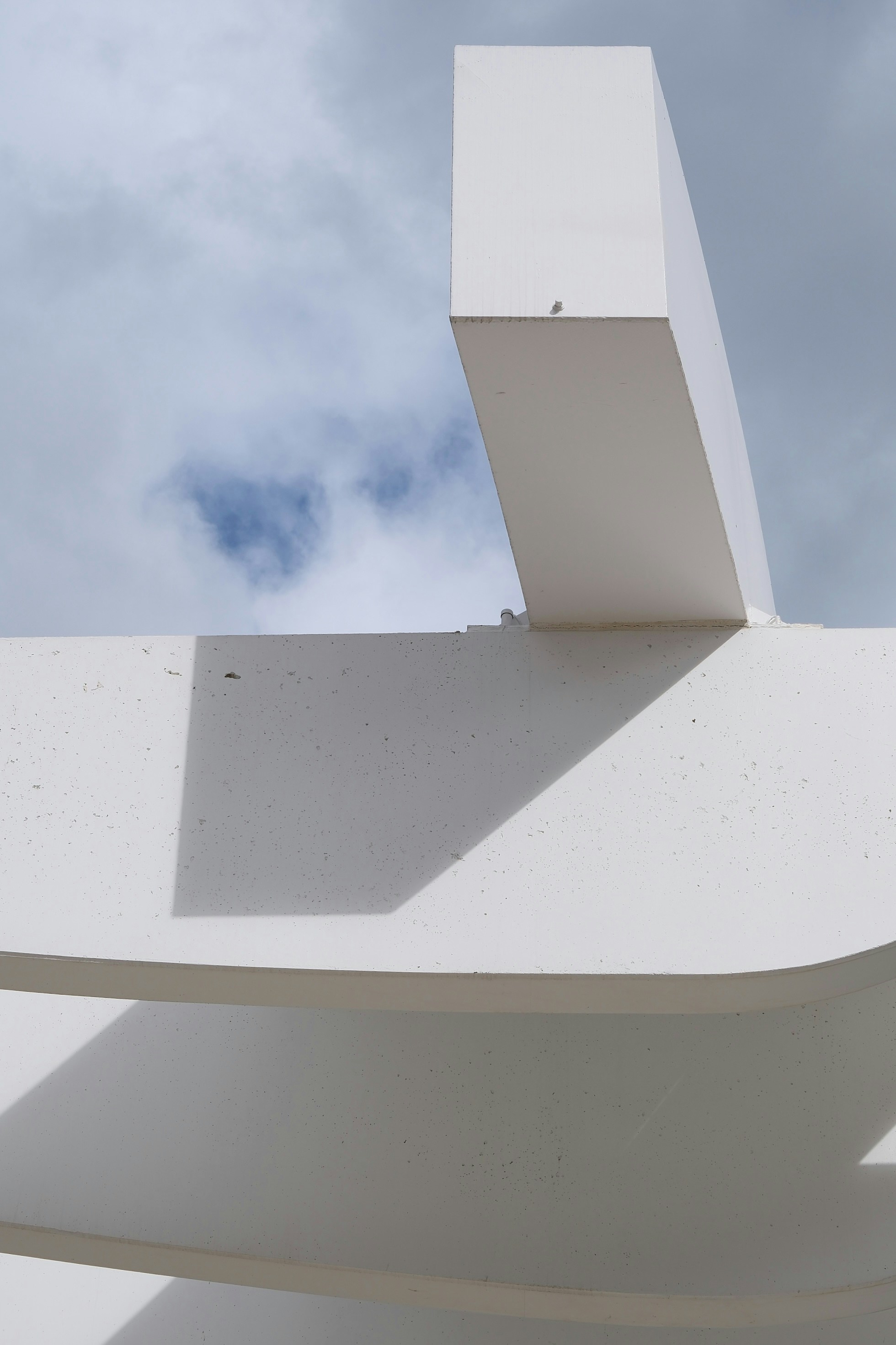 Angular white sculpture casting shadows under a pale blue sky