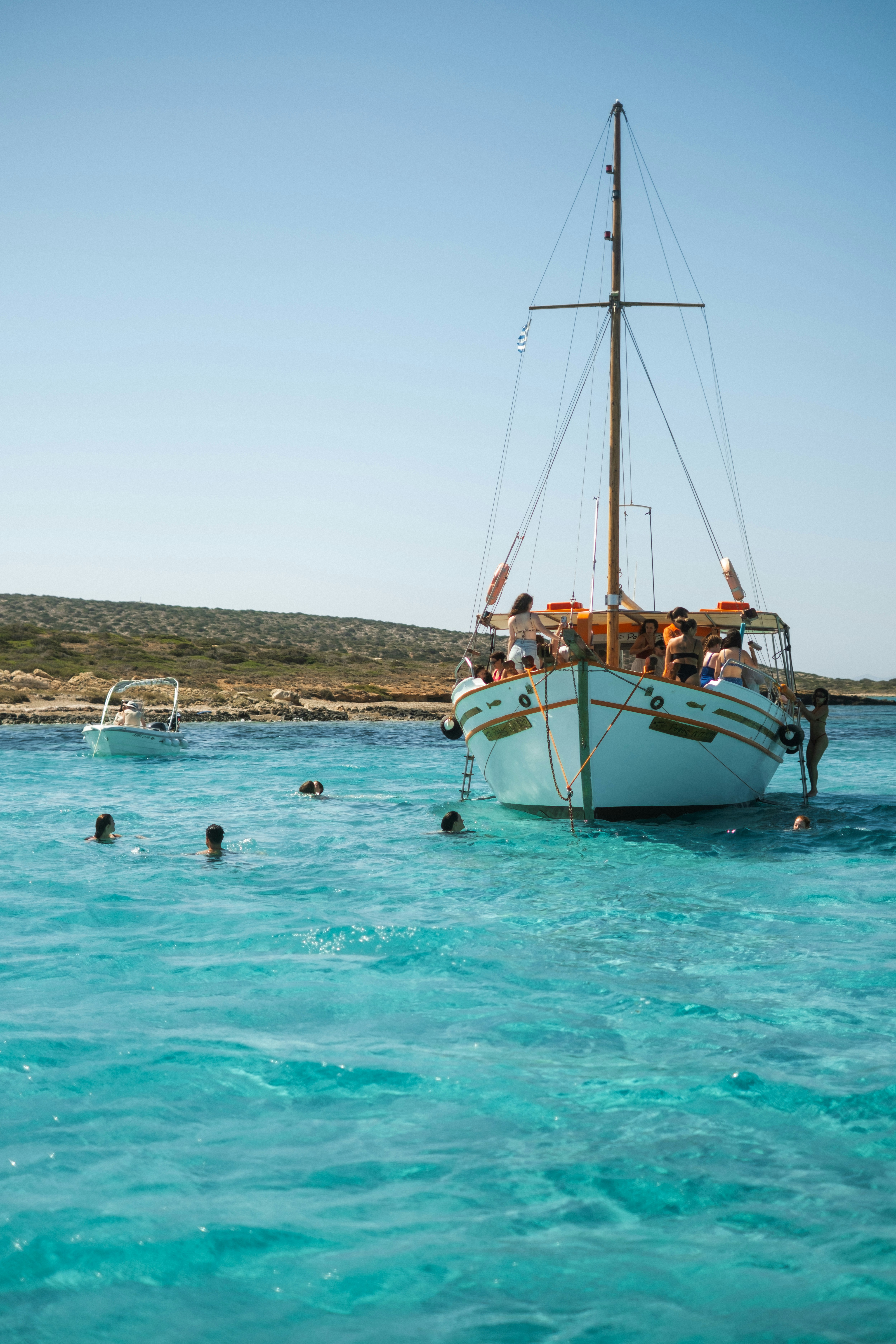 Sailboat at anchor in turquoise shallows, gathering swimmers at the bow