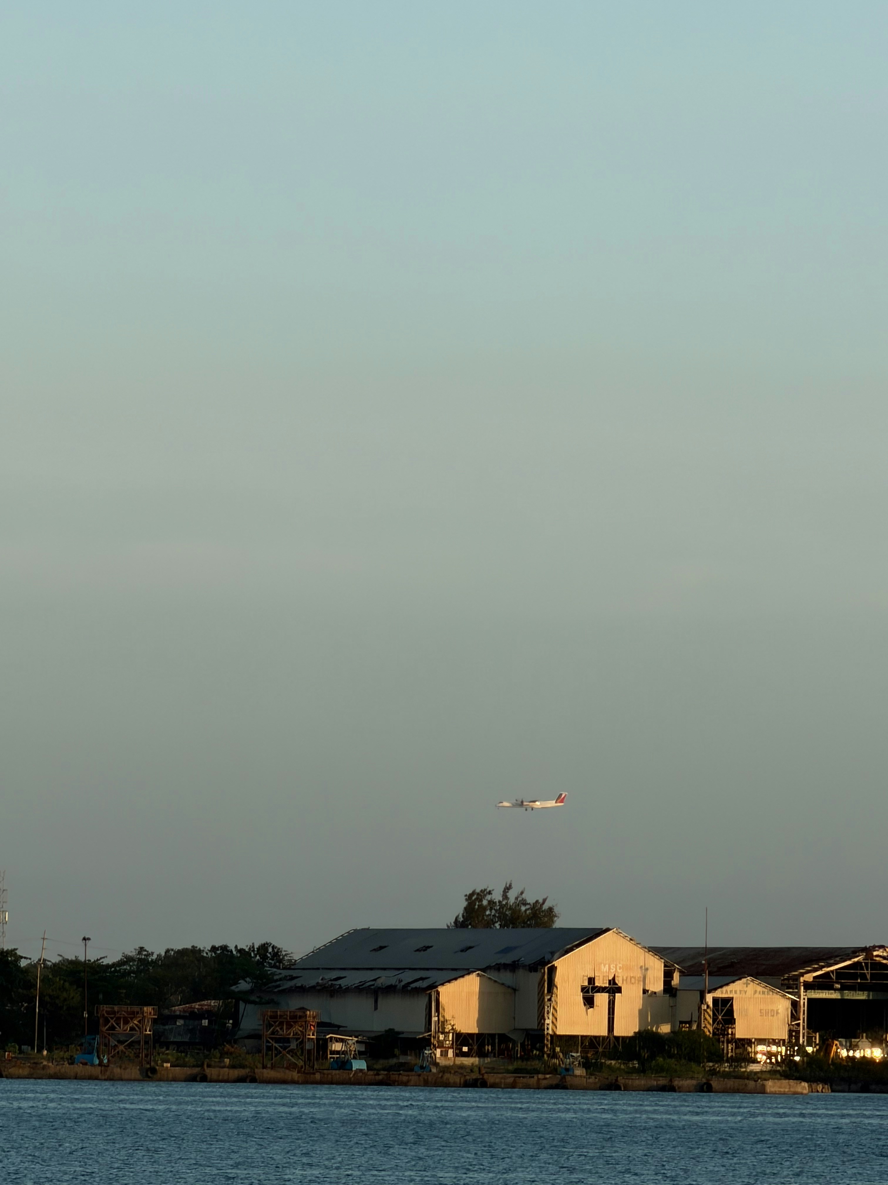 Airplane Rises Over Coastal Industrial Strip at Dusk