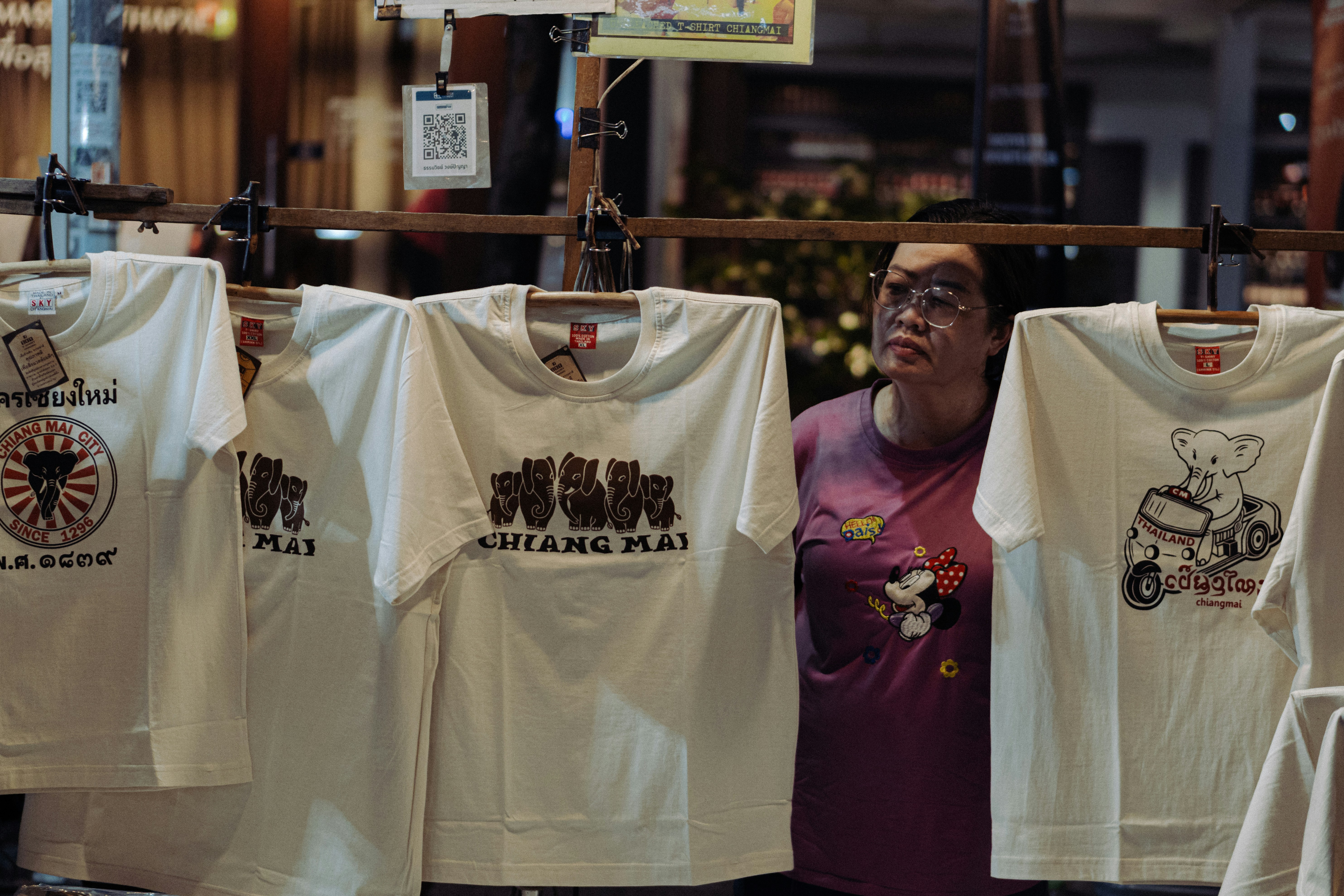 Vendor Behind Row of Tees: A Quiet Moment in the Market