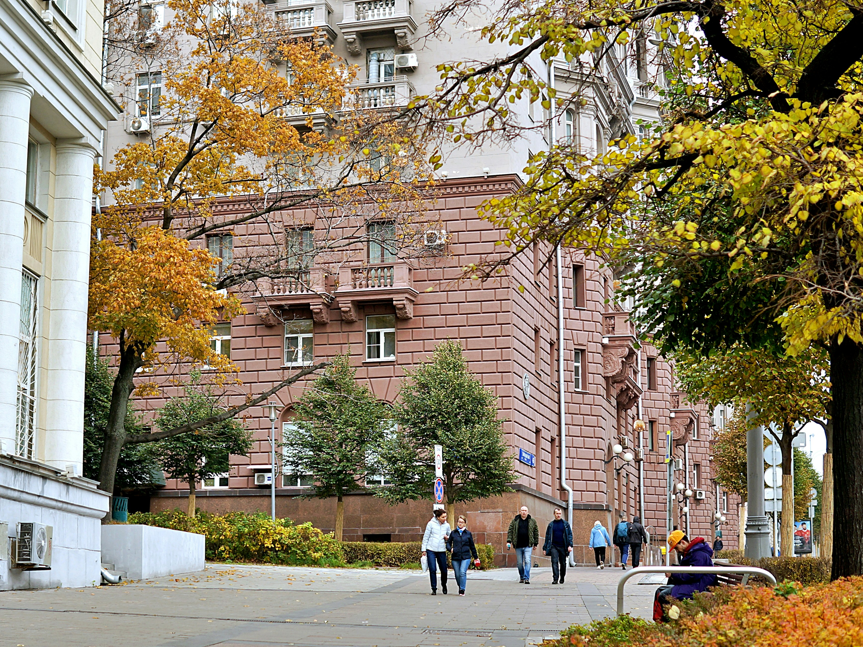 Autumn Boulevard: Brick Facade, Trees, and Pedestrians