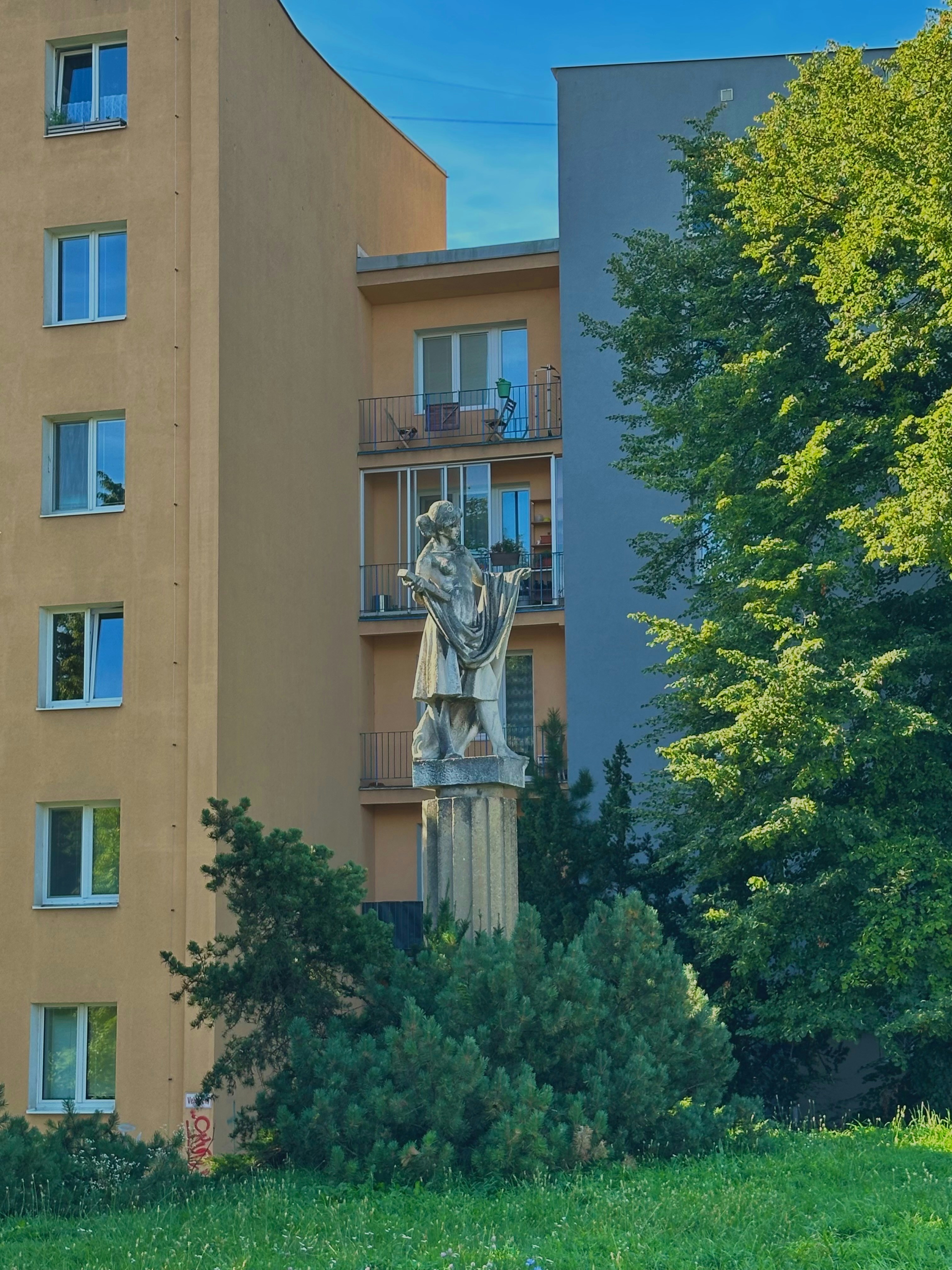 Statue Between Towers: A Quiet Monolith Overlooking a Green Margin