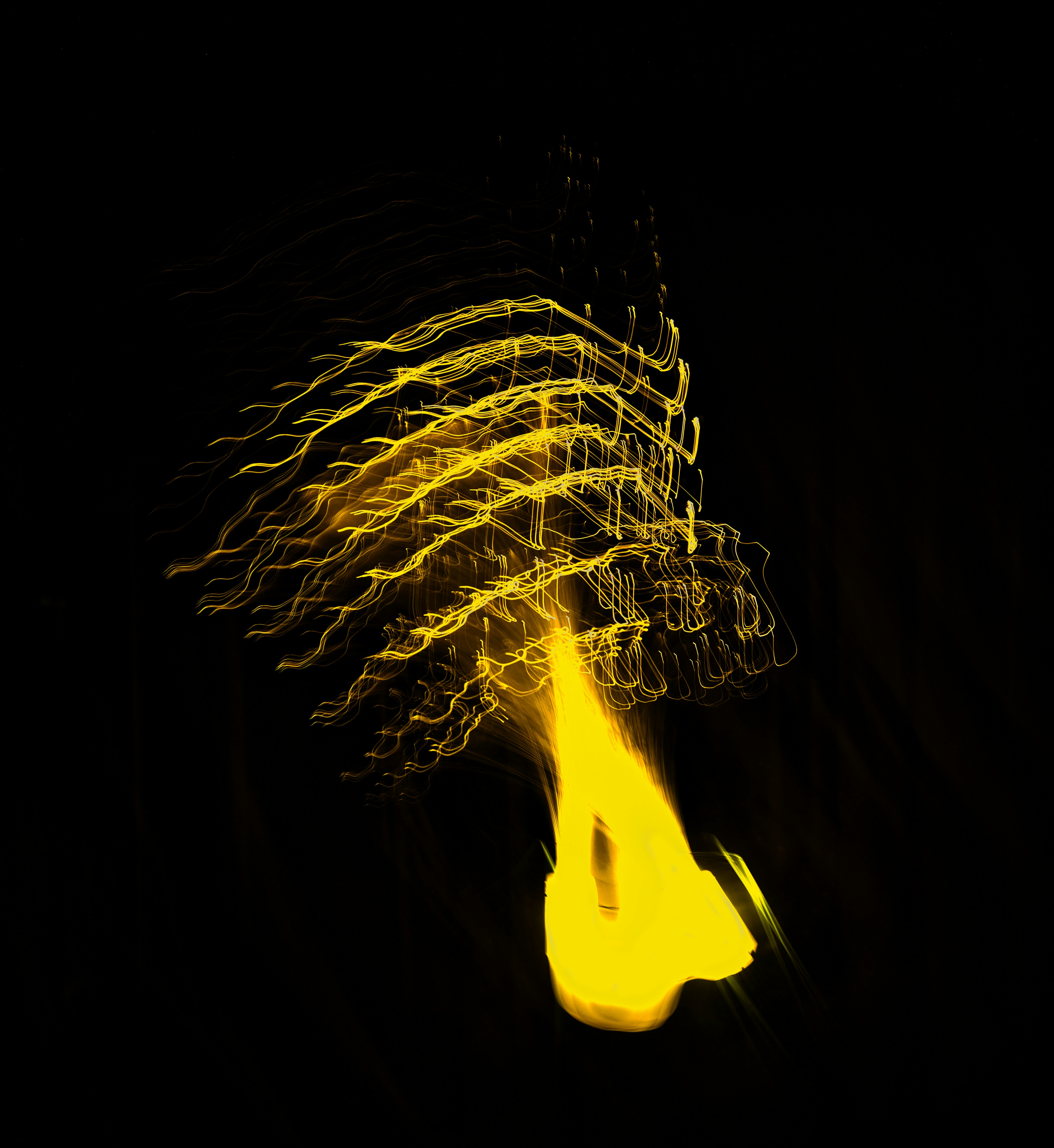 Abstract long-exposure of a yellow light source tracing, creating a dancer-like arc against a black background. This image emphasizes motion and luminous trails rather than a defined subject.