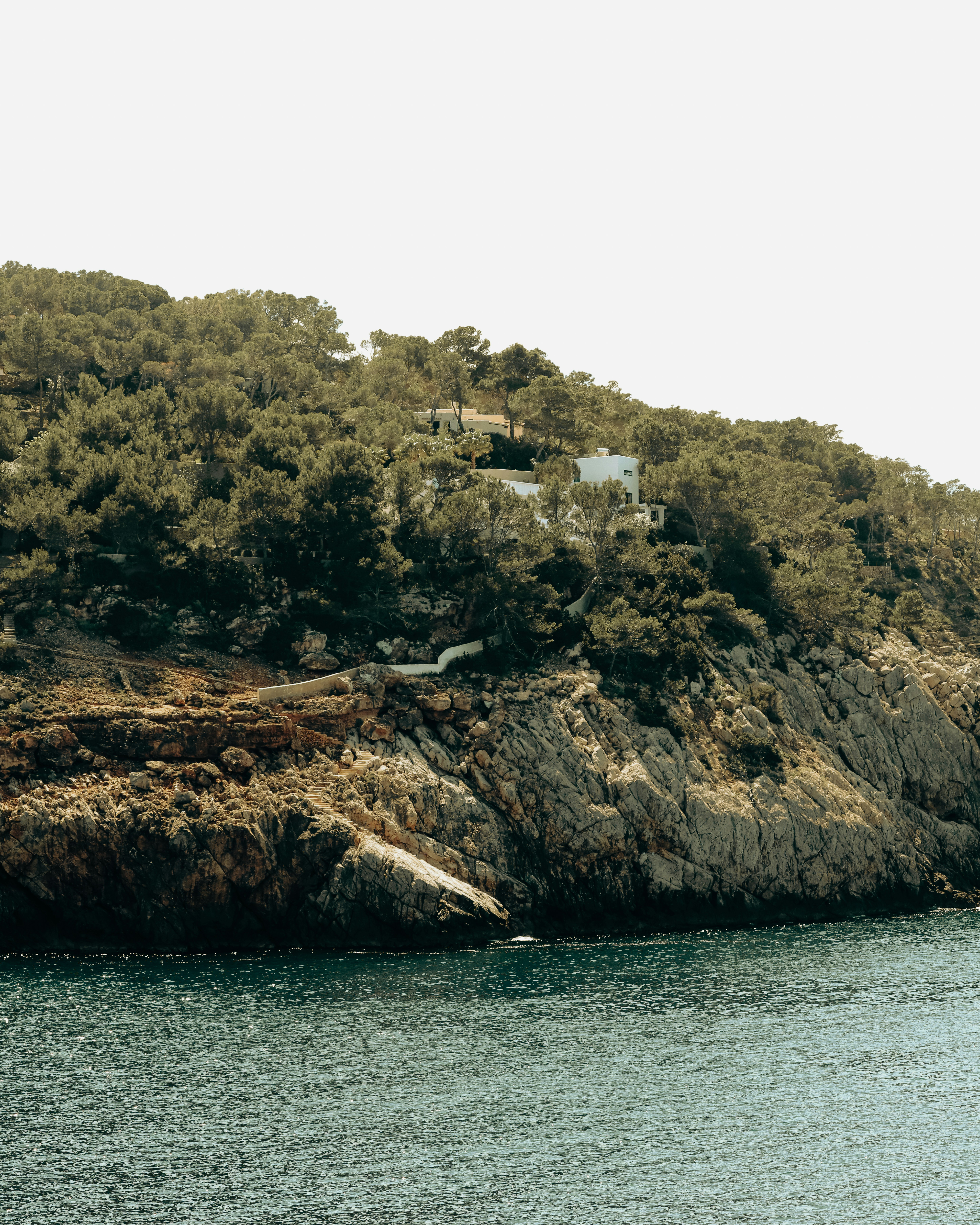 Coastal Cliff House Amidst Trees Overlooking Calm Sea