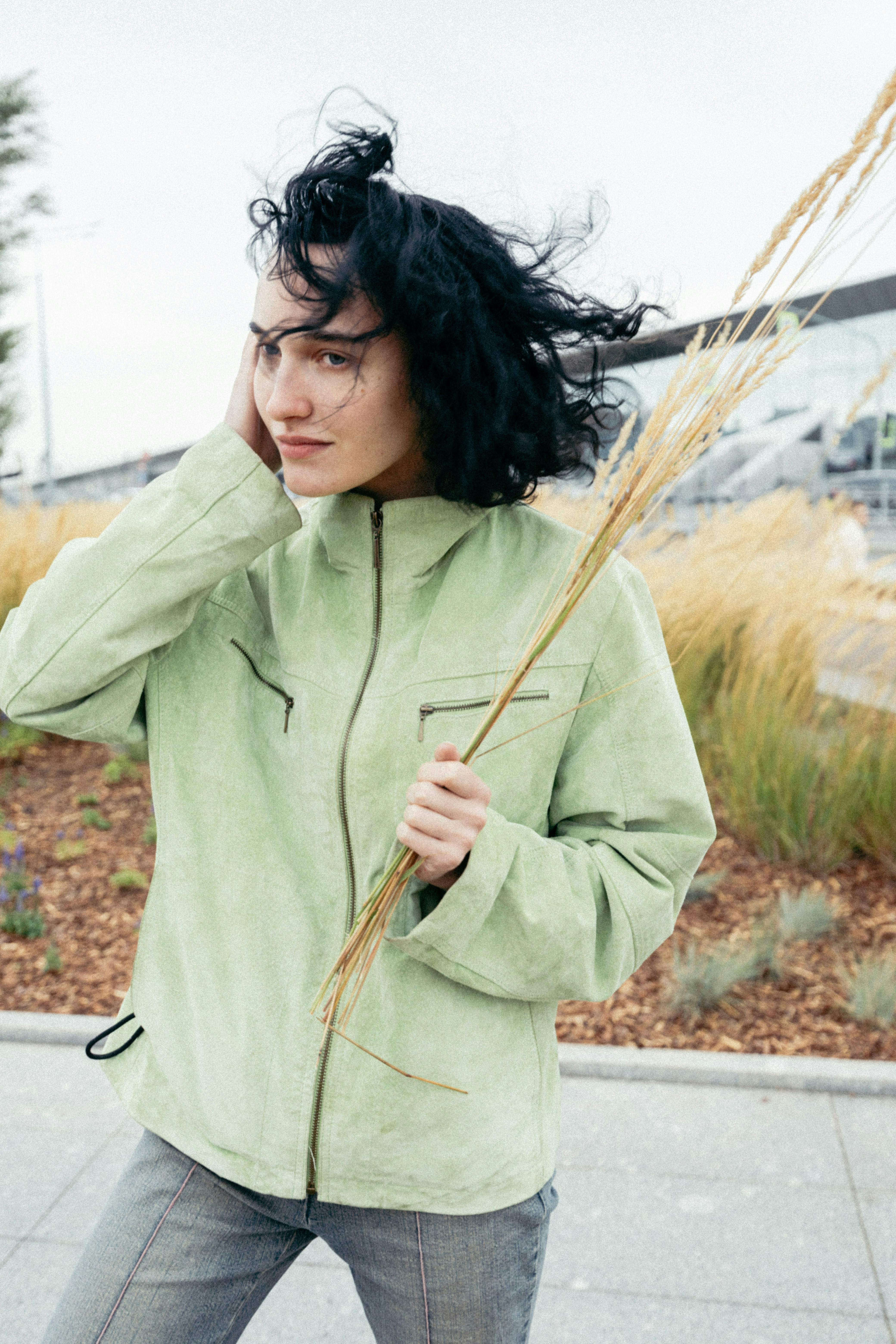Wind-swept portrait in a pale-green jacket amid tall grasses