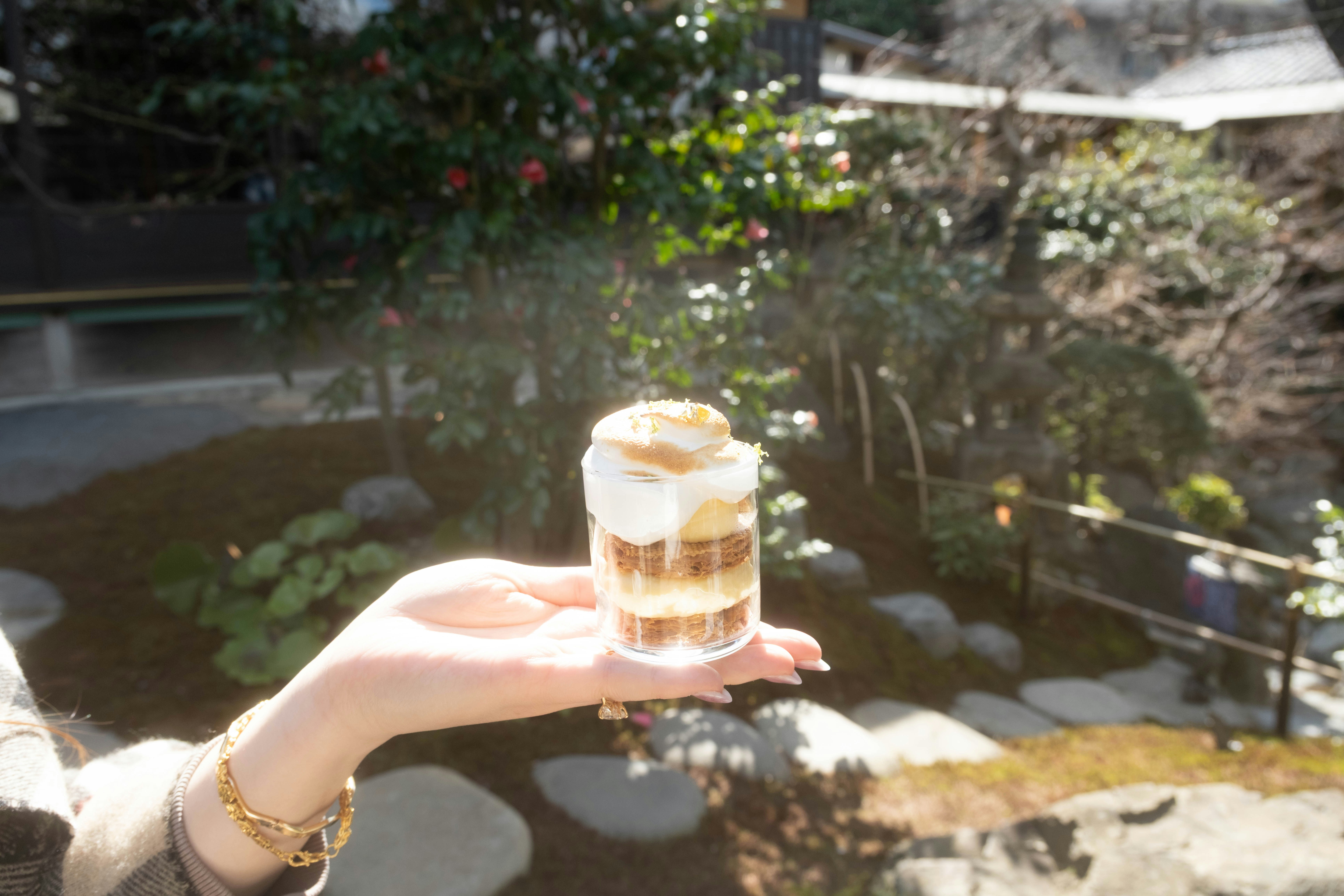 A hand holds a layered dessert in a glass
