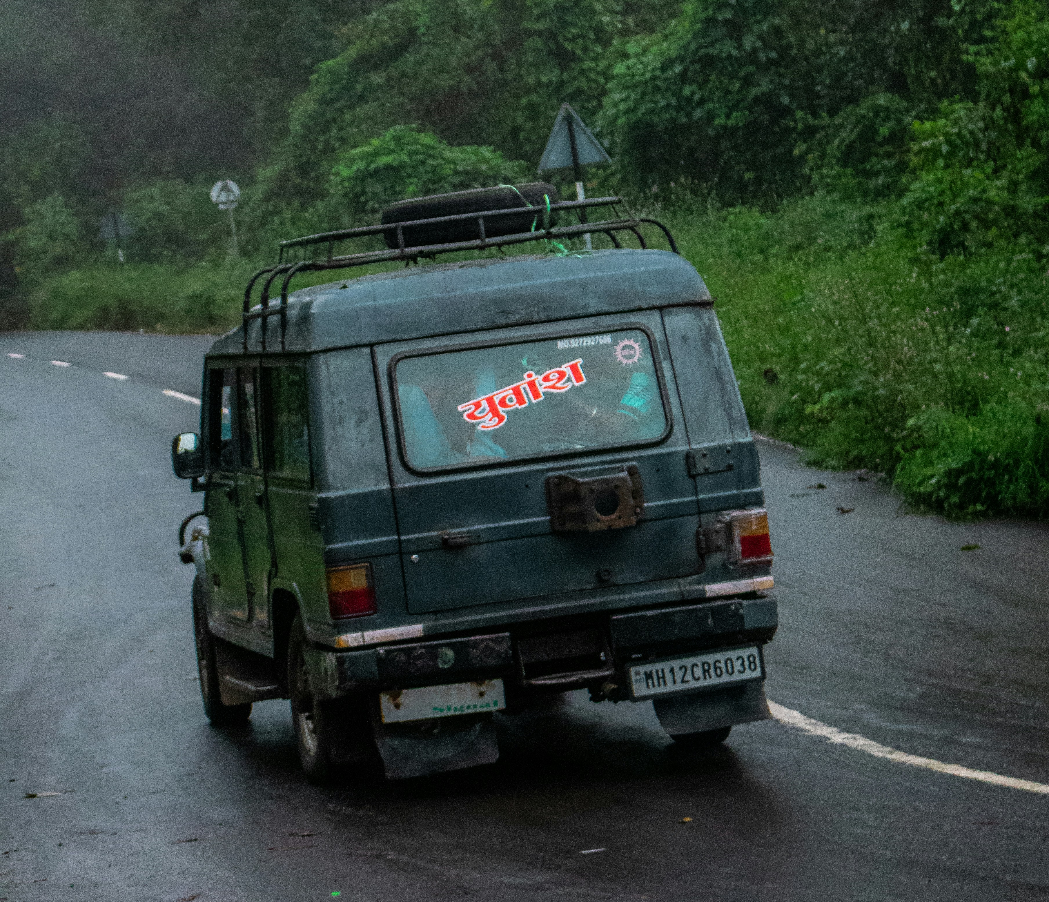Weathered blue van on a winding rural road with lush greenery